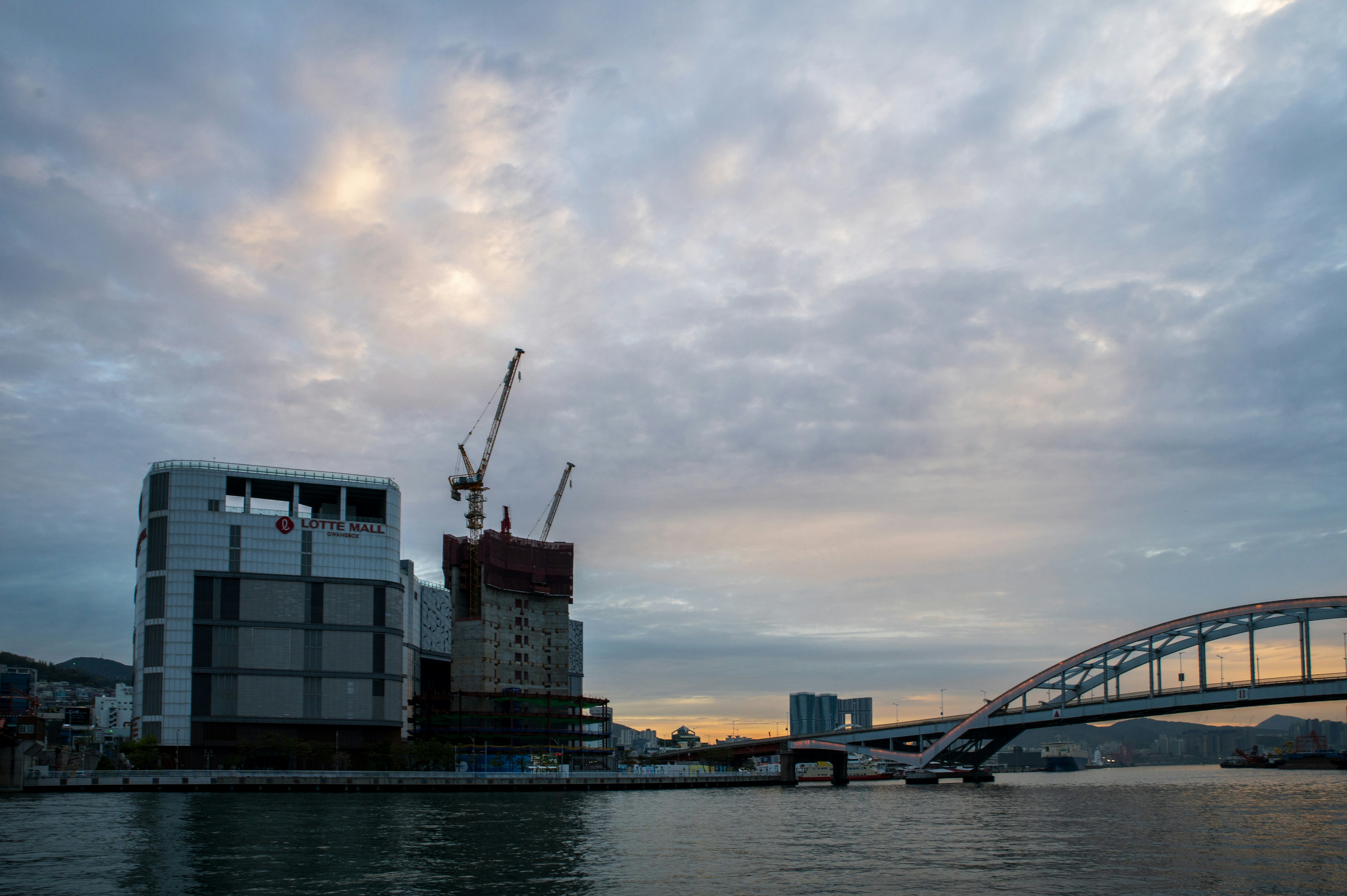 Rising cranes over a riverside skyline at dusk