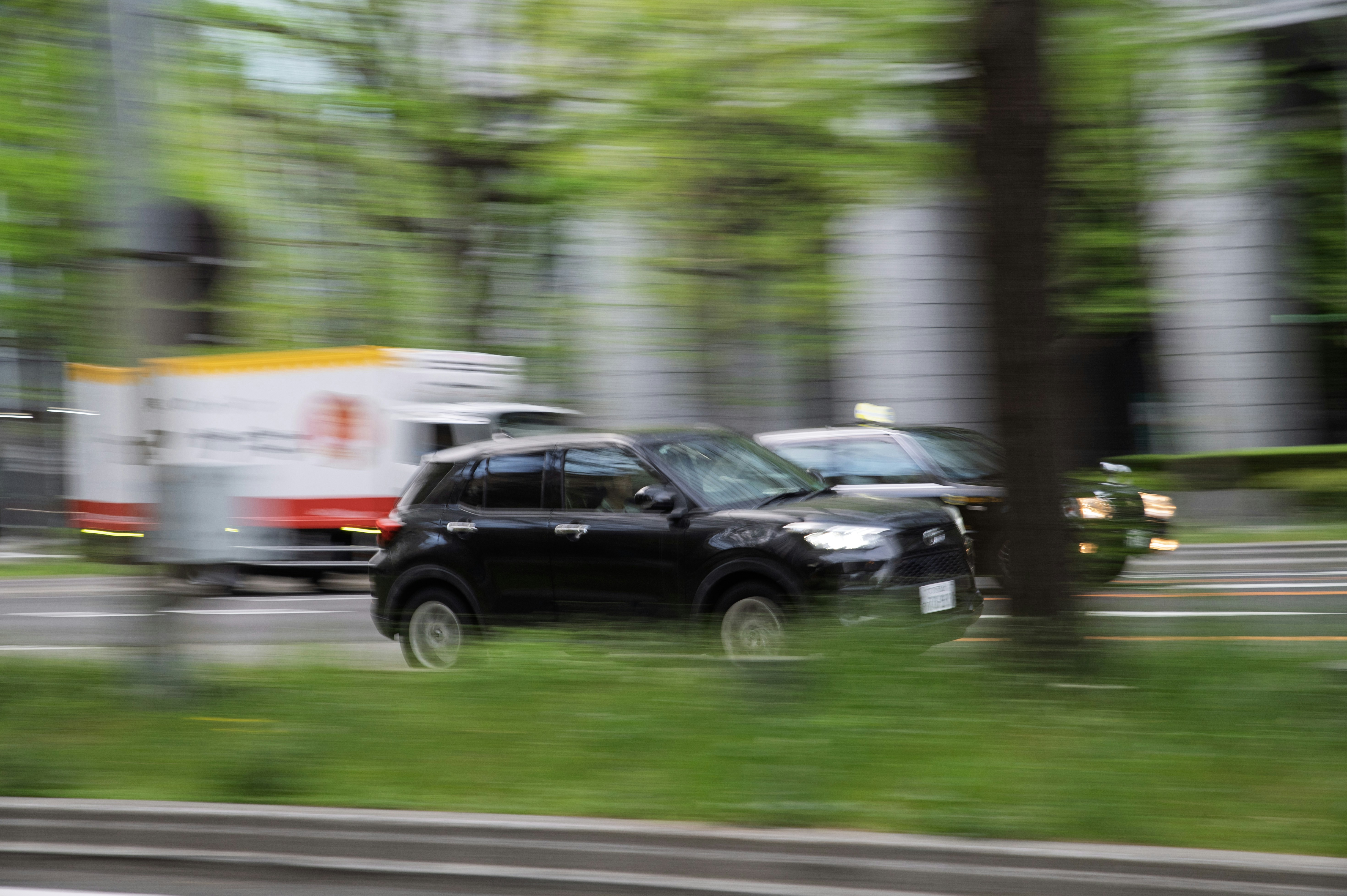 Blurry Pursuit: A Black SUV Speeds by on a Green Corridor