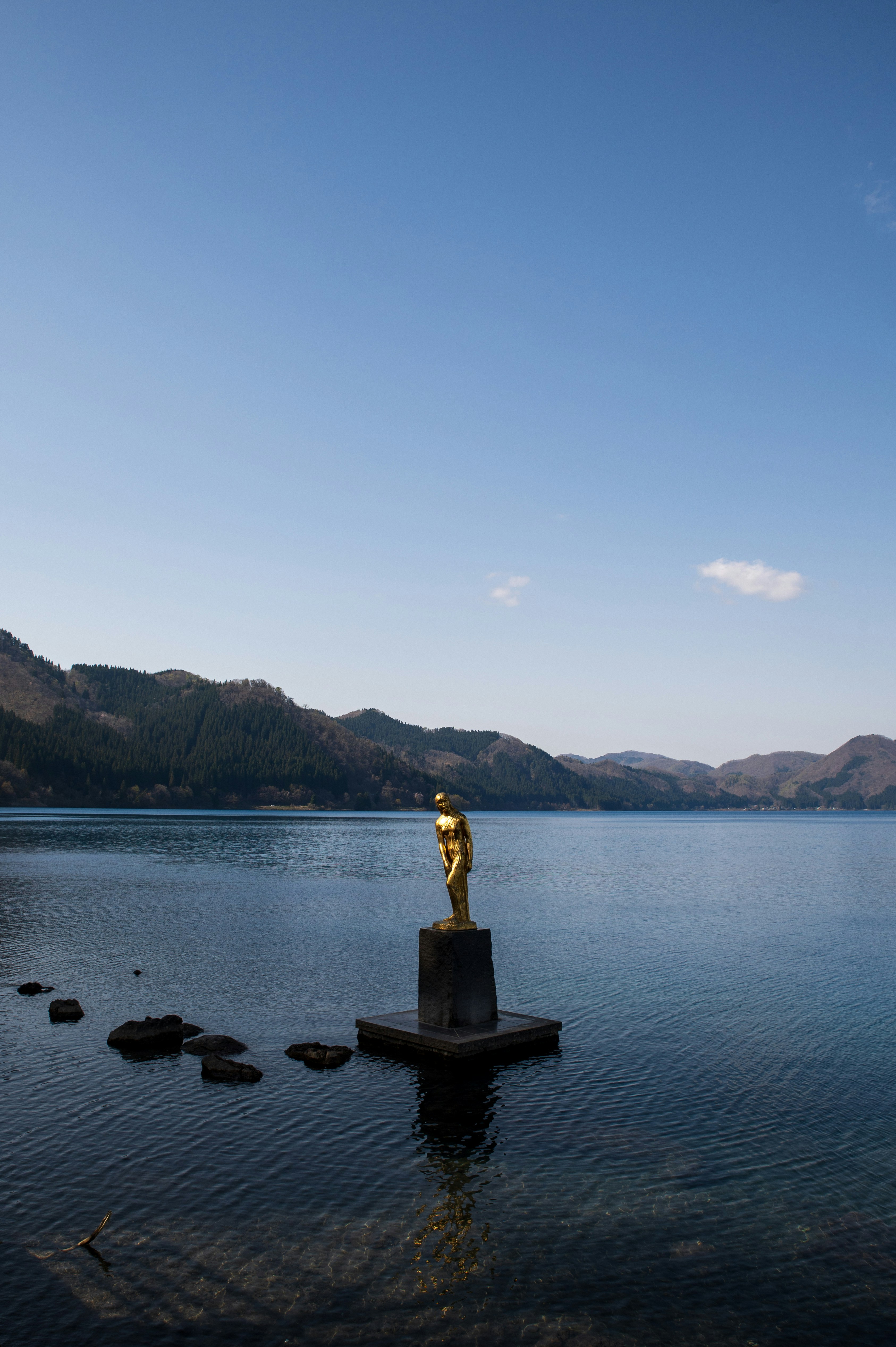 Golden Sentinel on the Lake: A Solitary Statue against a Serene Mountain Horizon