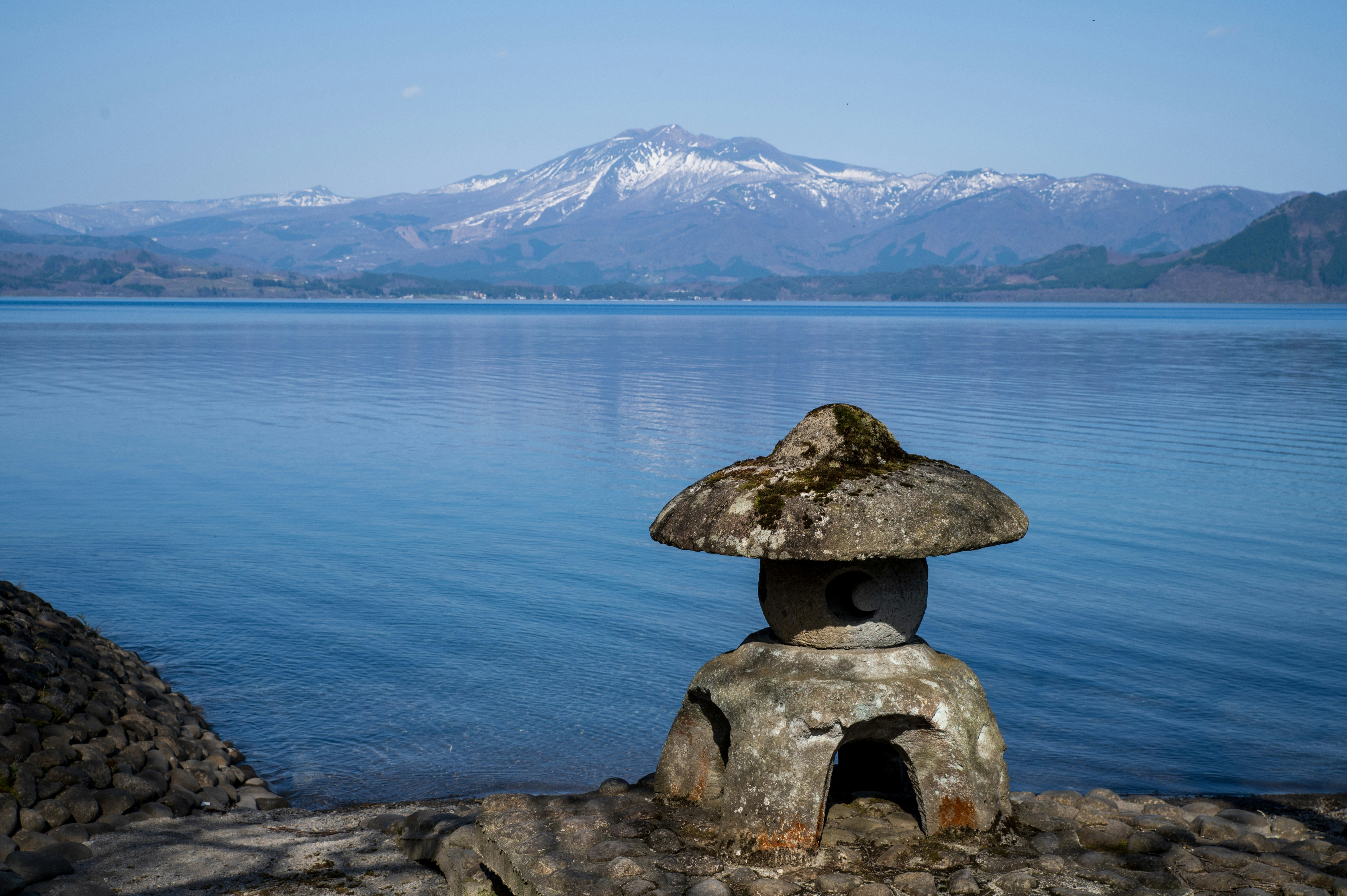 Lone Stone Lantern by a Serene Blue Lake with Snow-Capped Peaks