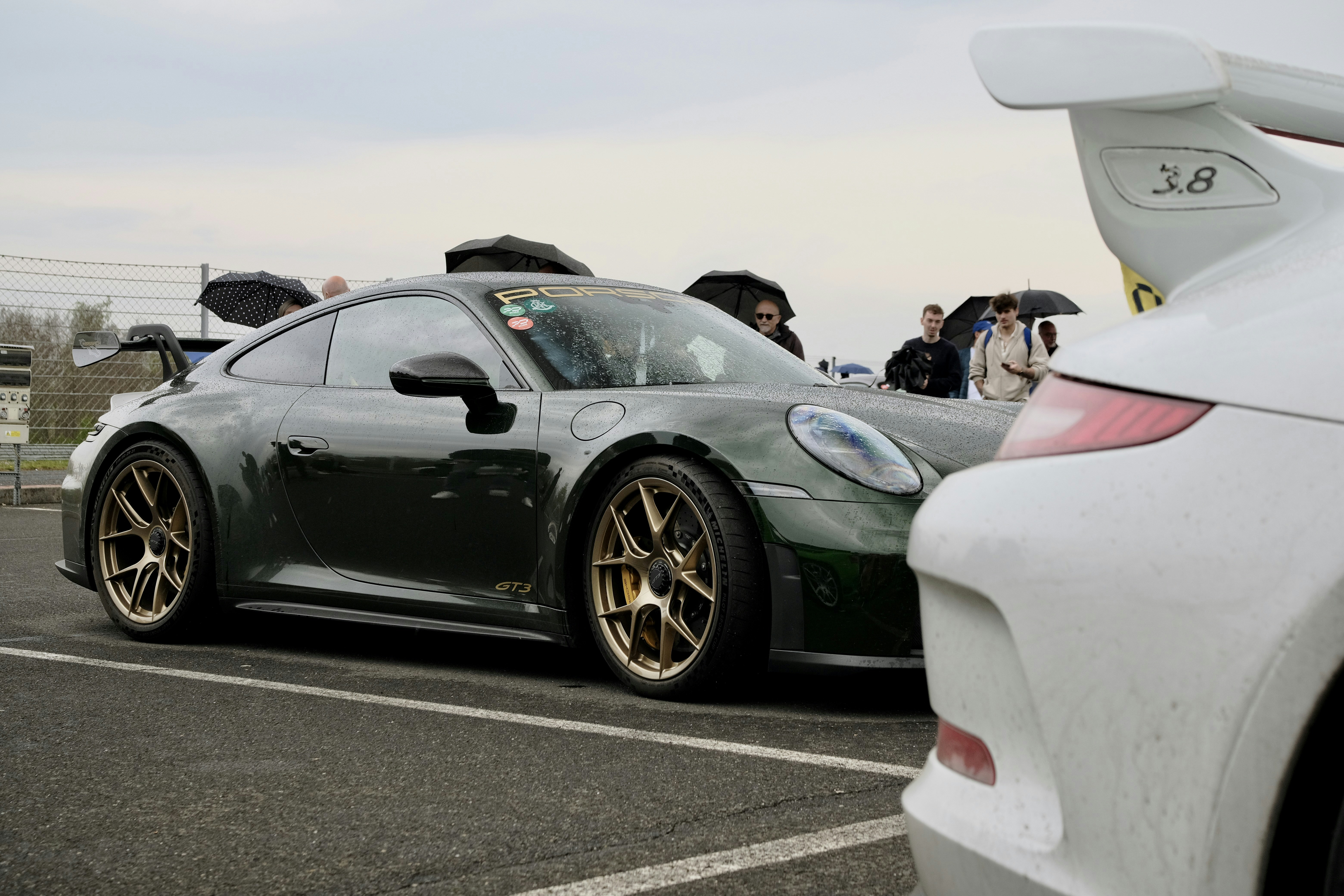 Midnight Green Porsche Stance at a Club Raceway, Framed by a Bright White Wing