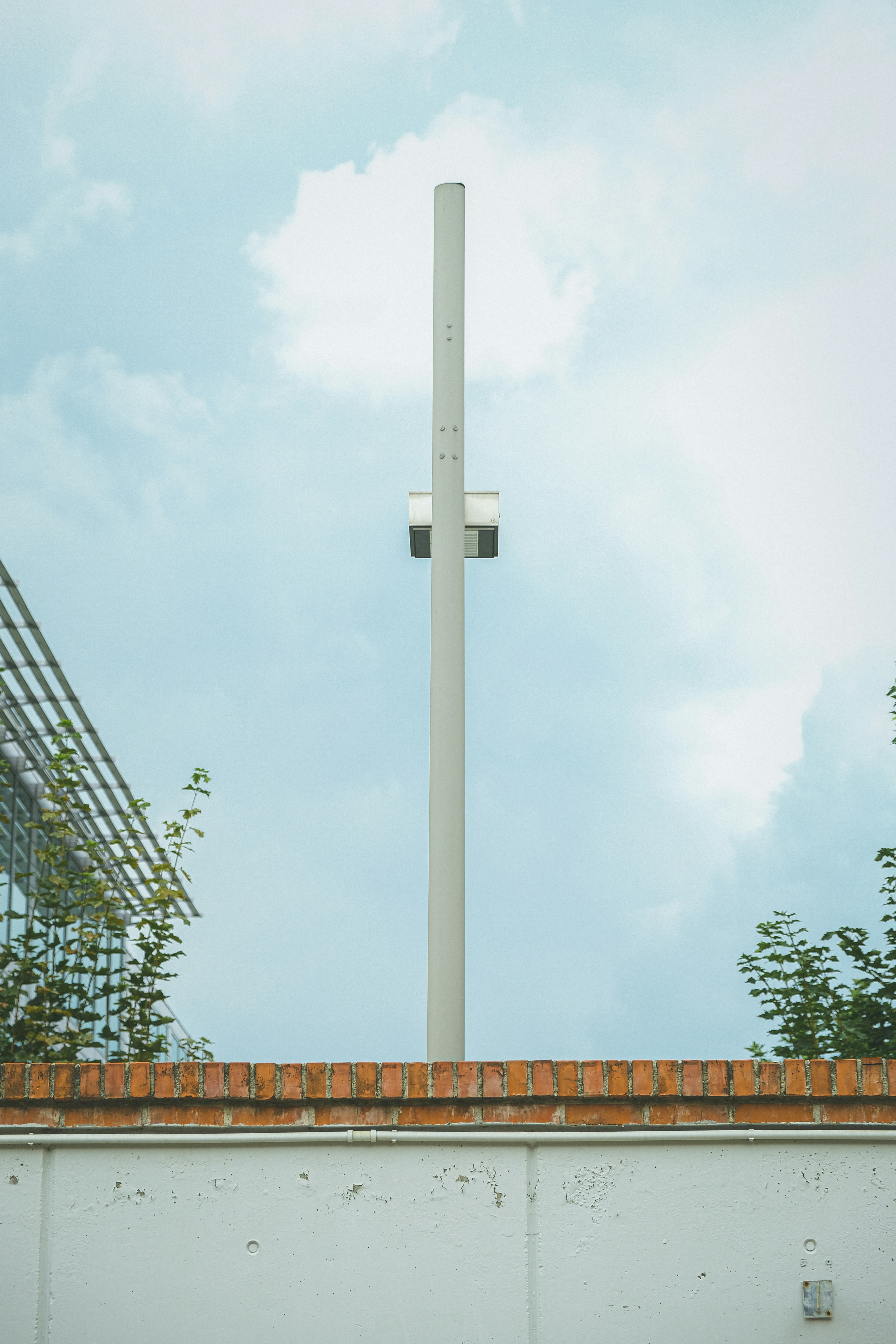 A lone street lamp rises above a low brick wall against a pale blue sky