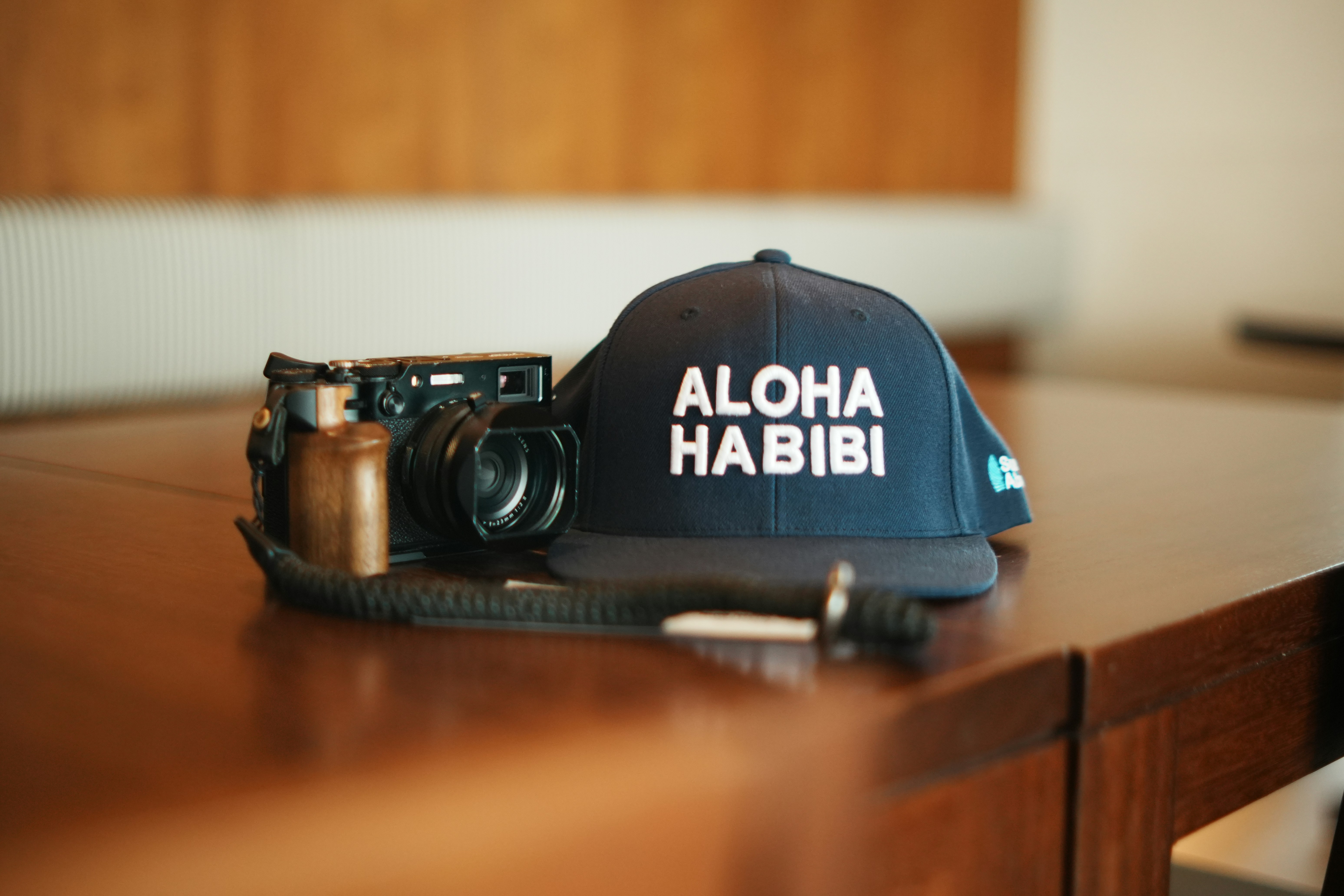 ALOHA HABIBI Keepsake: A Retro Camera and Cap Rest on a Wooden Table