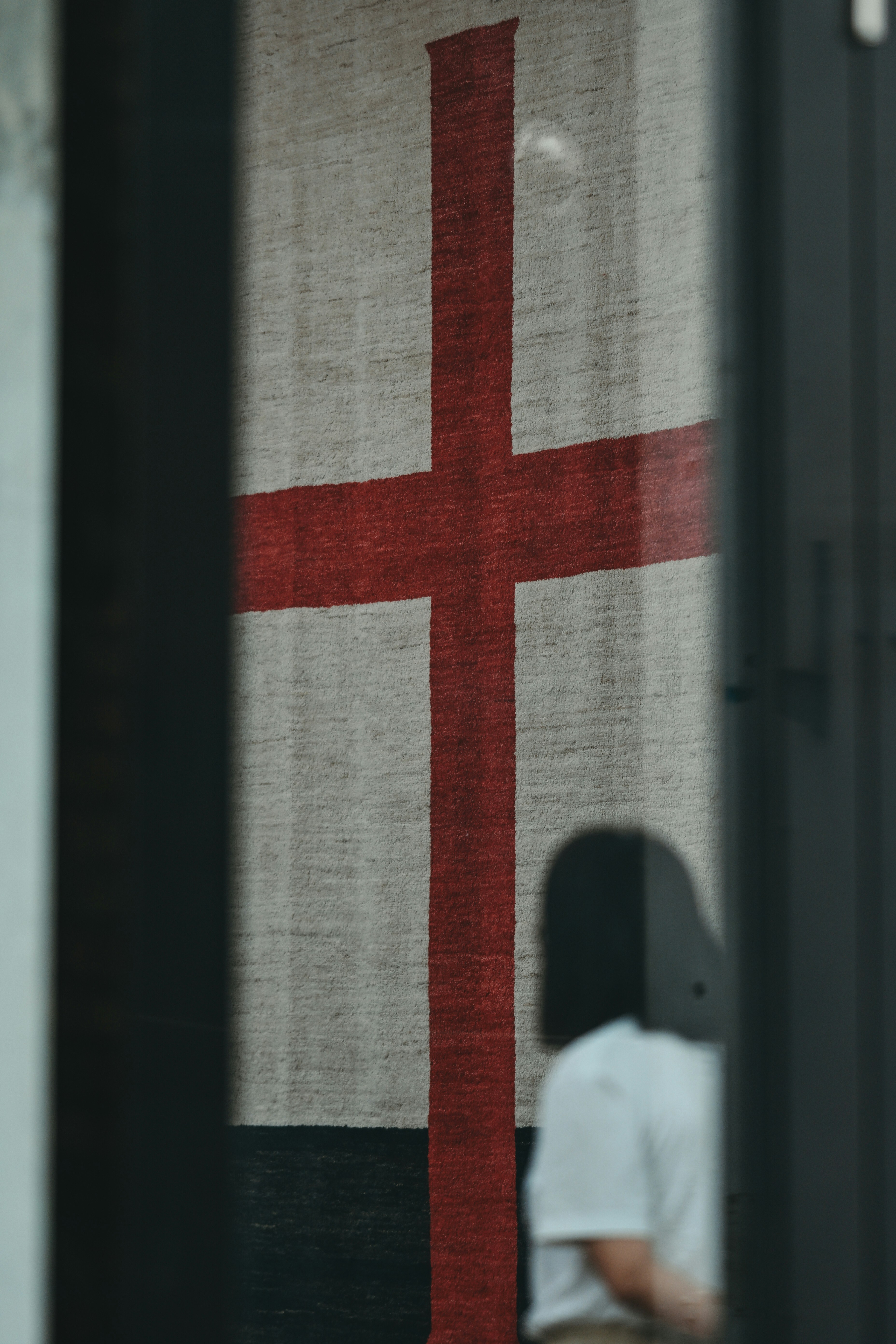 Crossing Shadows: A Narrow View of a Red Cross in Concrete