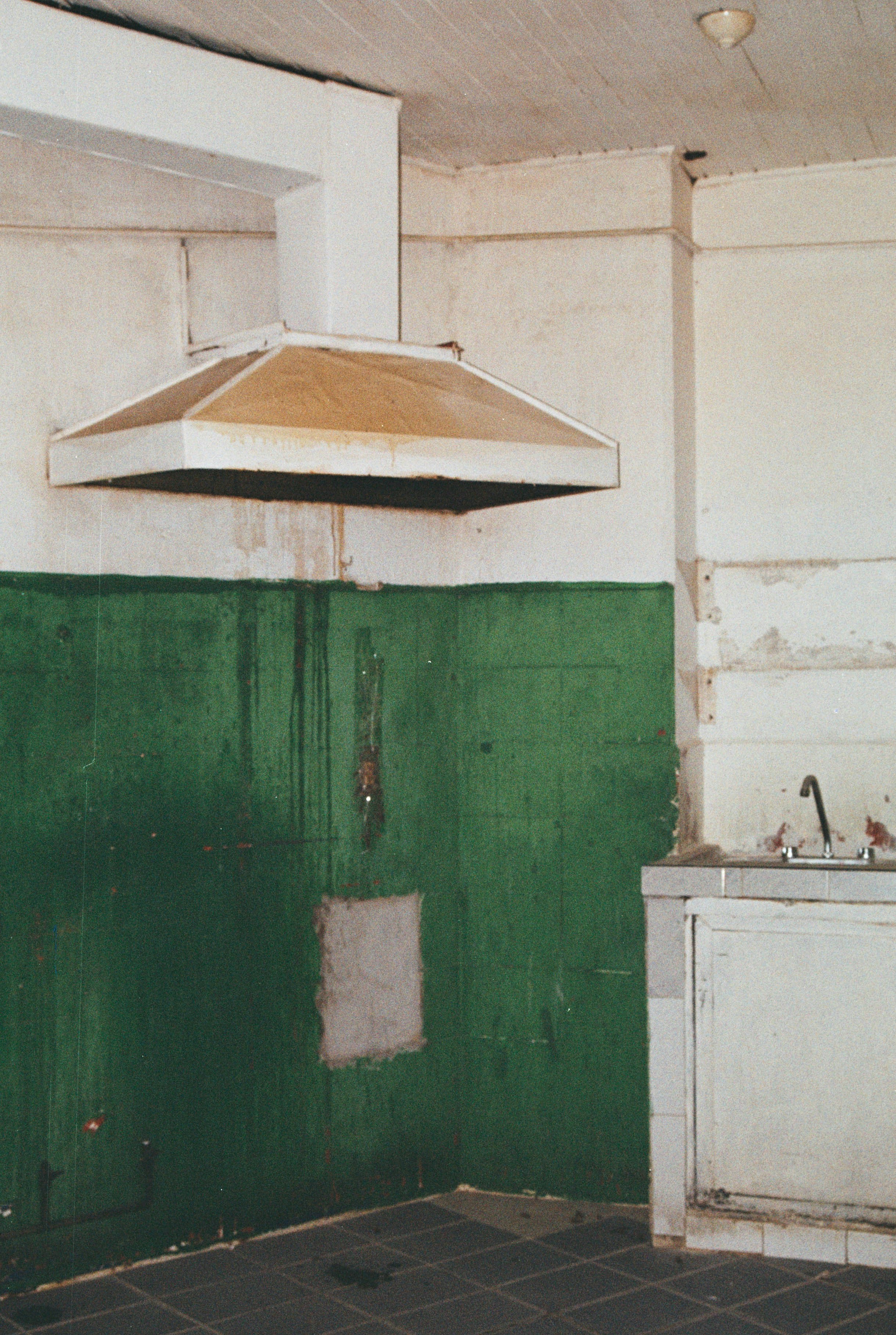 Abandoned Kitchen at Dusk: A Rusted Green Remnant Beneath an Off-Center Hood