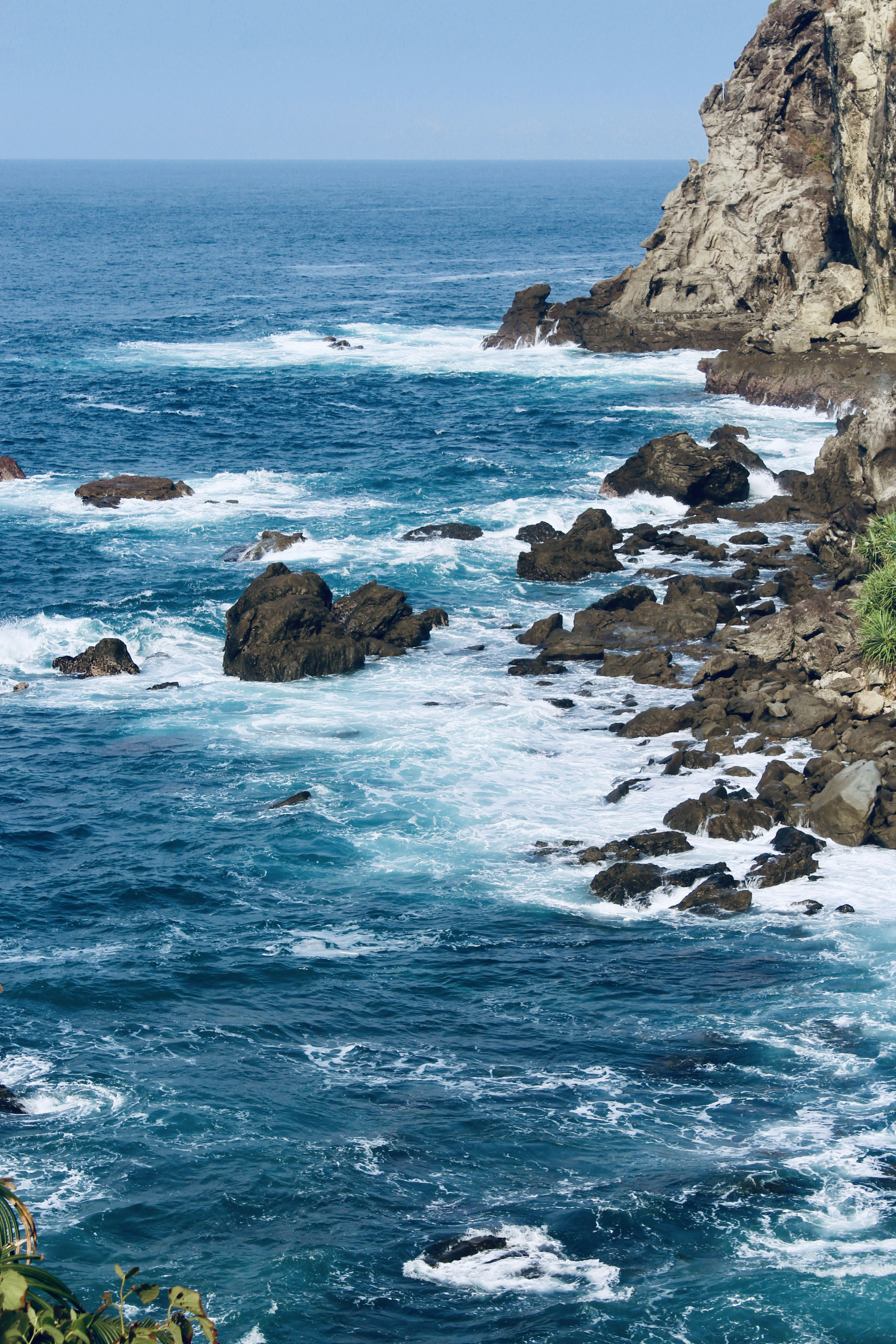 Rugged Coastline: Blue Waves Meet jagged Rocks under a Clear Sky
