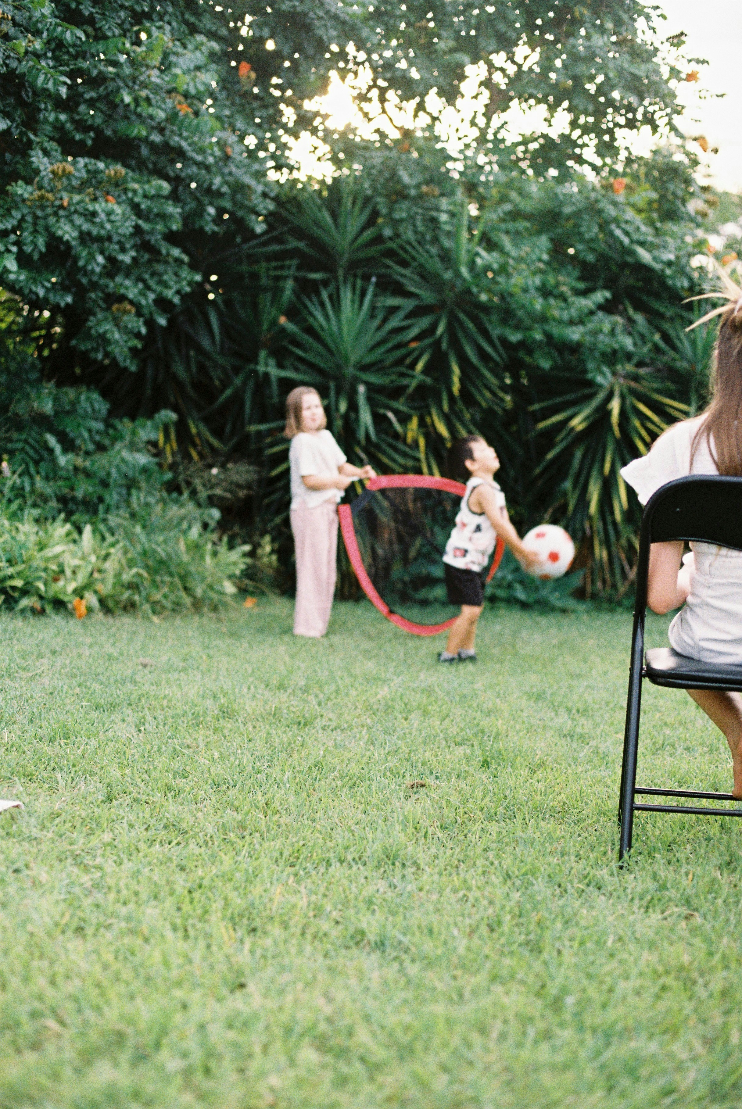 Children at play in a sunlit backyard with a looping red hoop