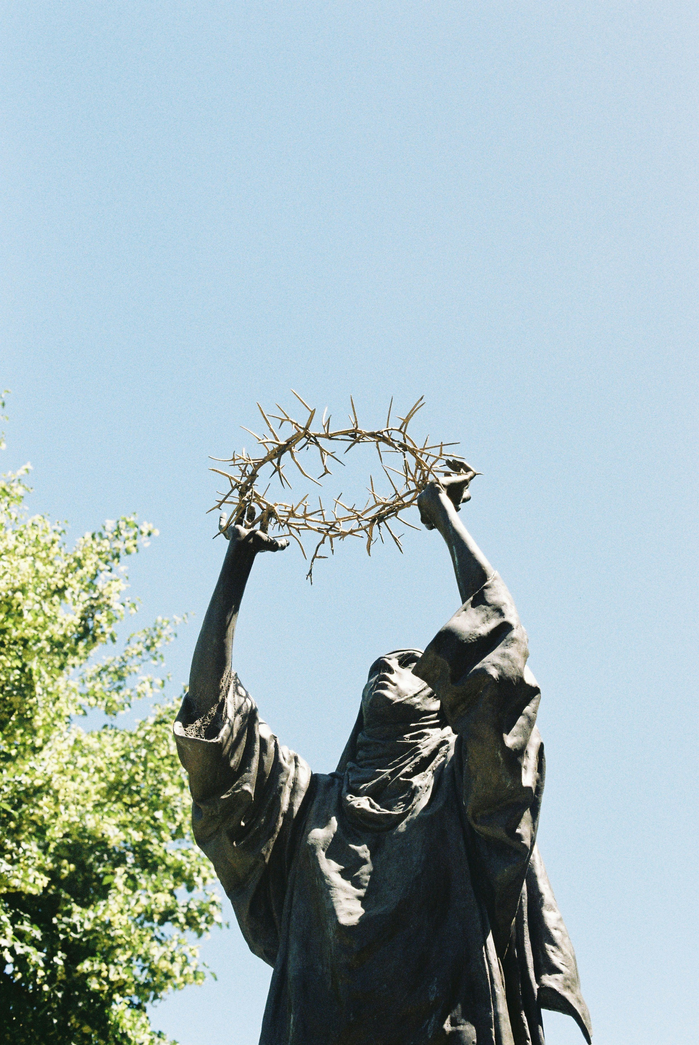 Statue holding a crown of thorns against blue sky