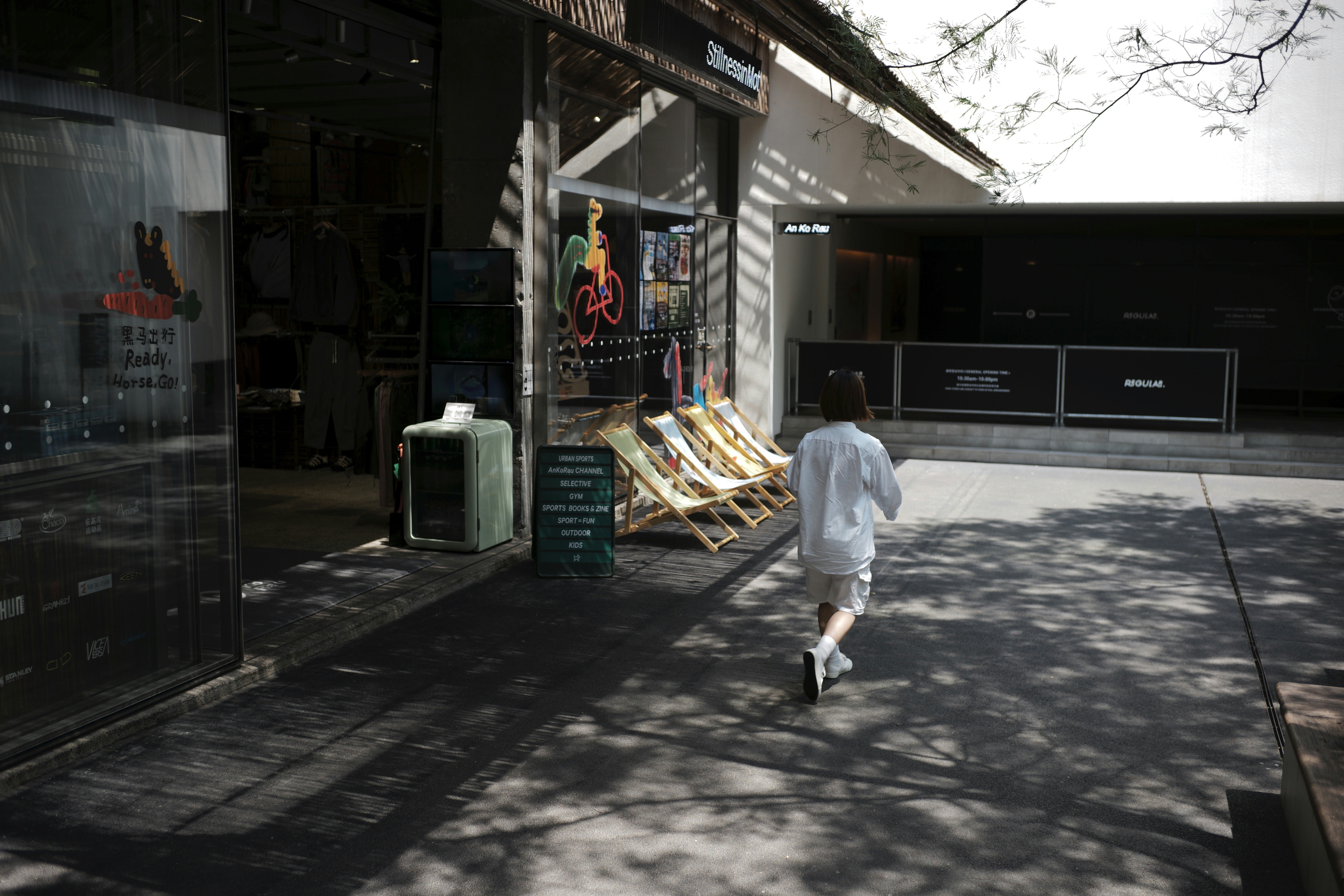 Child in White Chase Along Shaded Shopfront Corridor