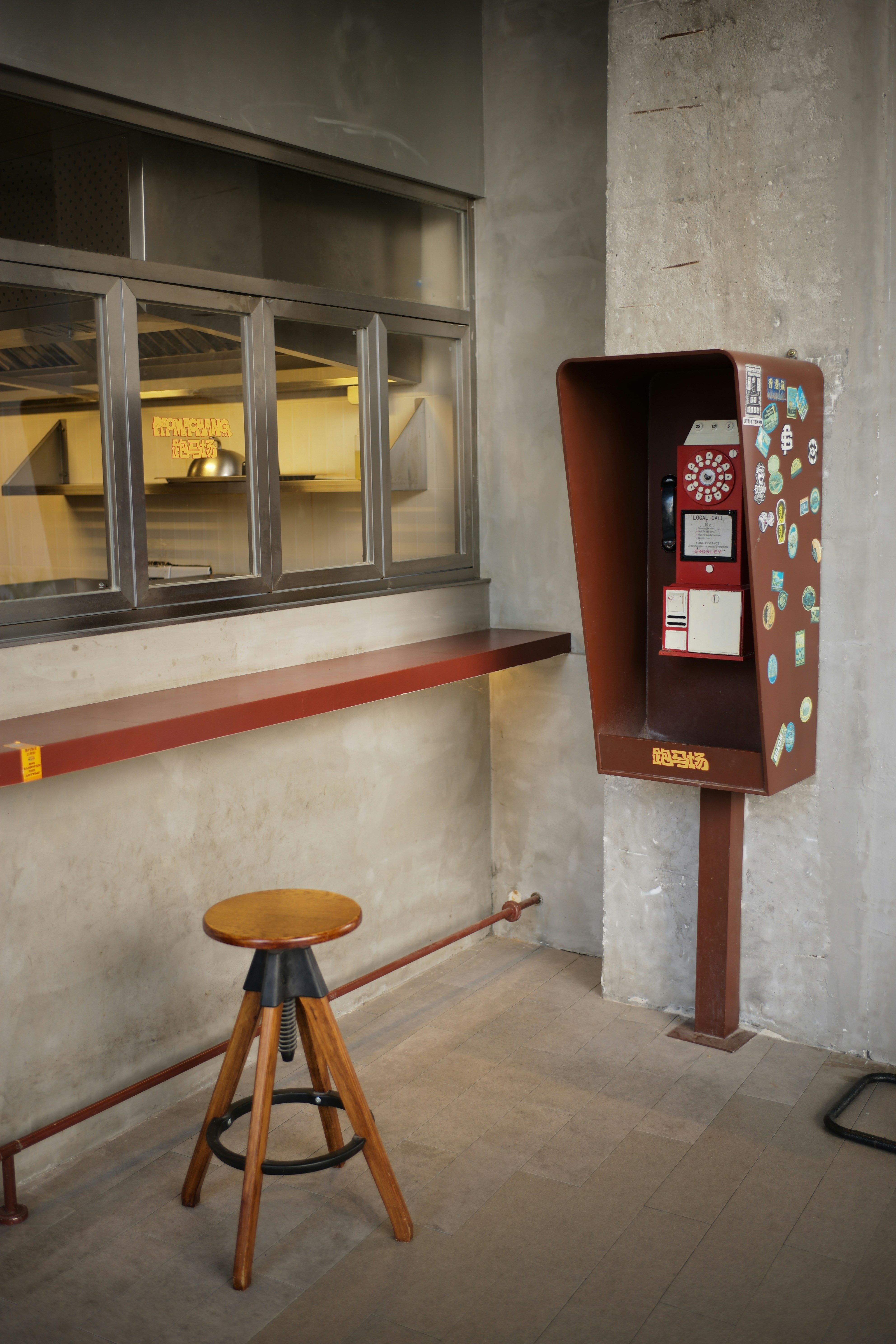 Quiet Corner of an Industrial Café: Stool, Window, and a Stickered Payphone