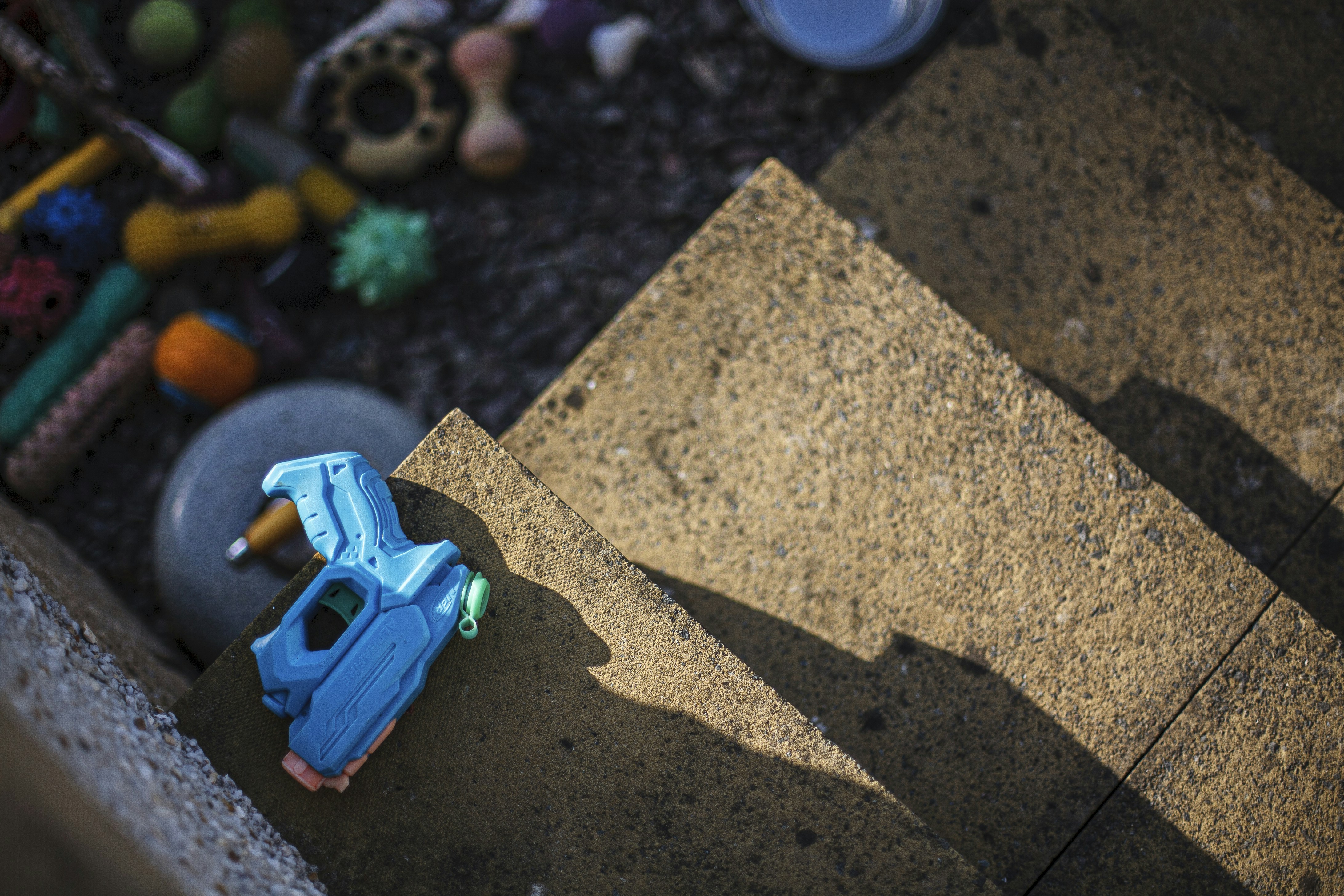 Blue toy car perched on sunlit concrete stairs amid scattered playthings