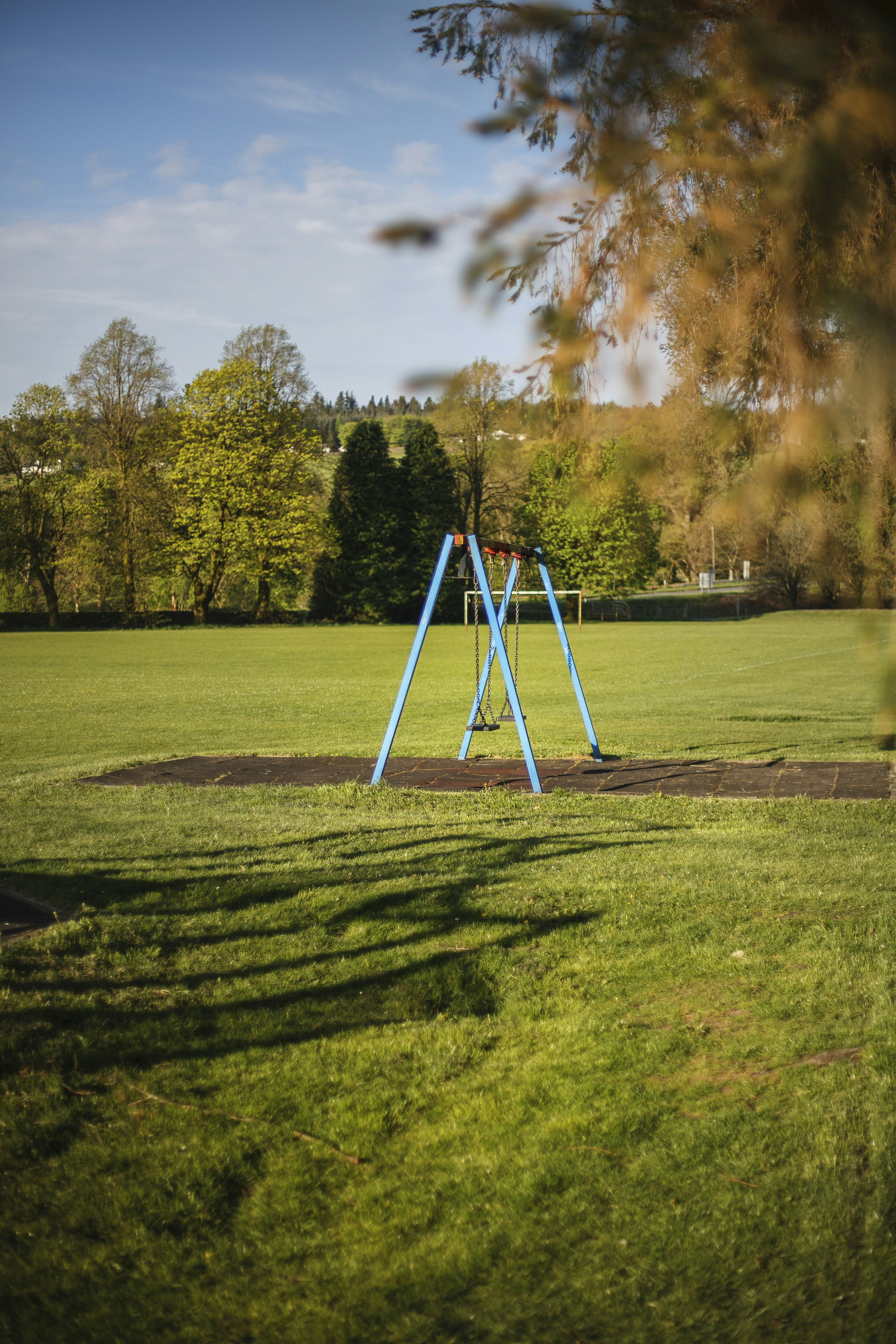 Blue Swing Set in Sunny Park with Distant Trees