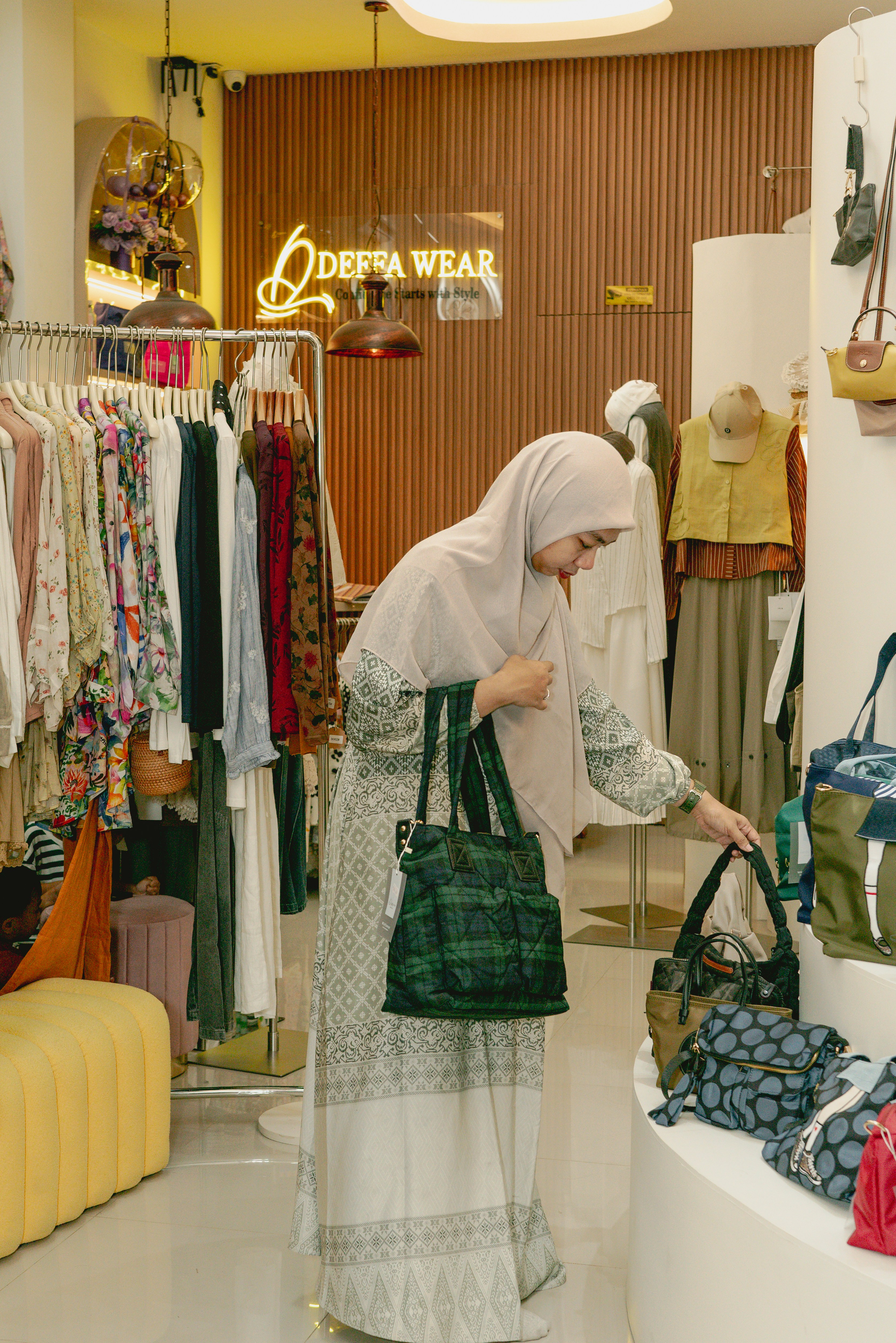 Hijab-clad shopper selecting a green bag in a chic boutique