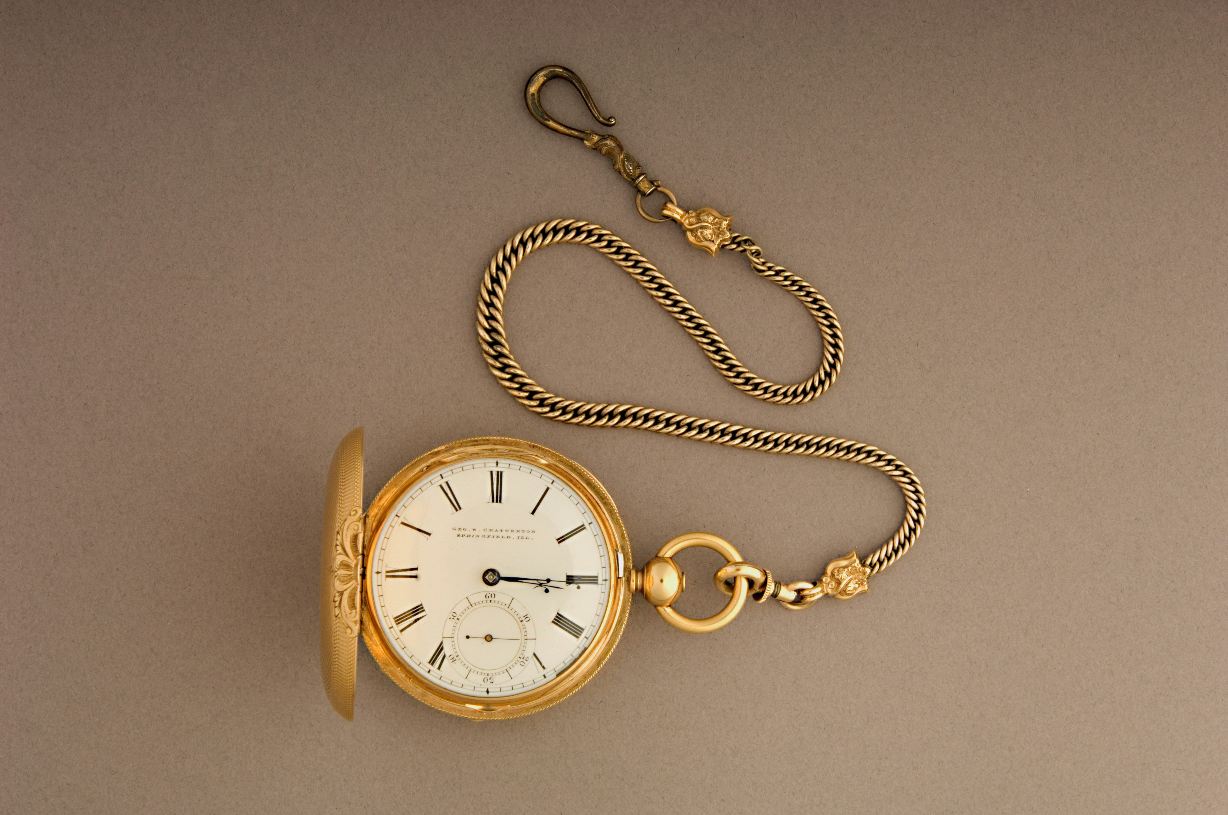 Gilded Timekeeper: A Gold Pocket Watch on a Rich Taupe Backdrop