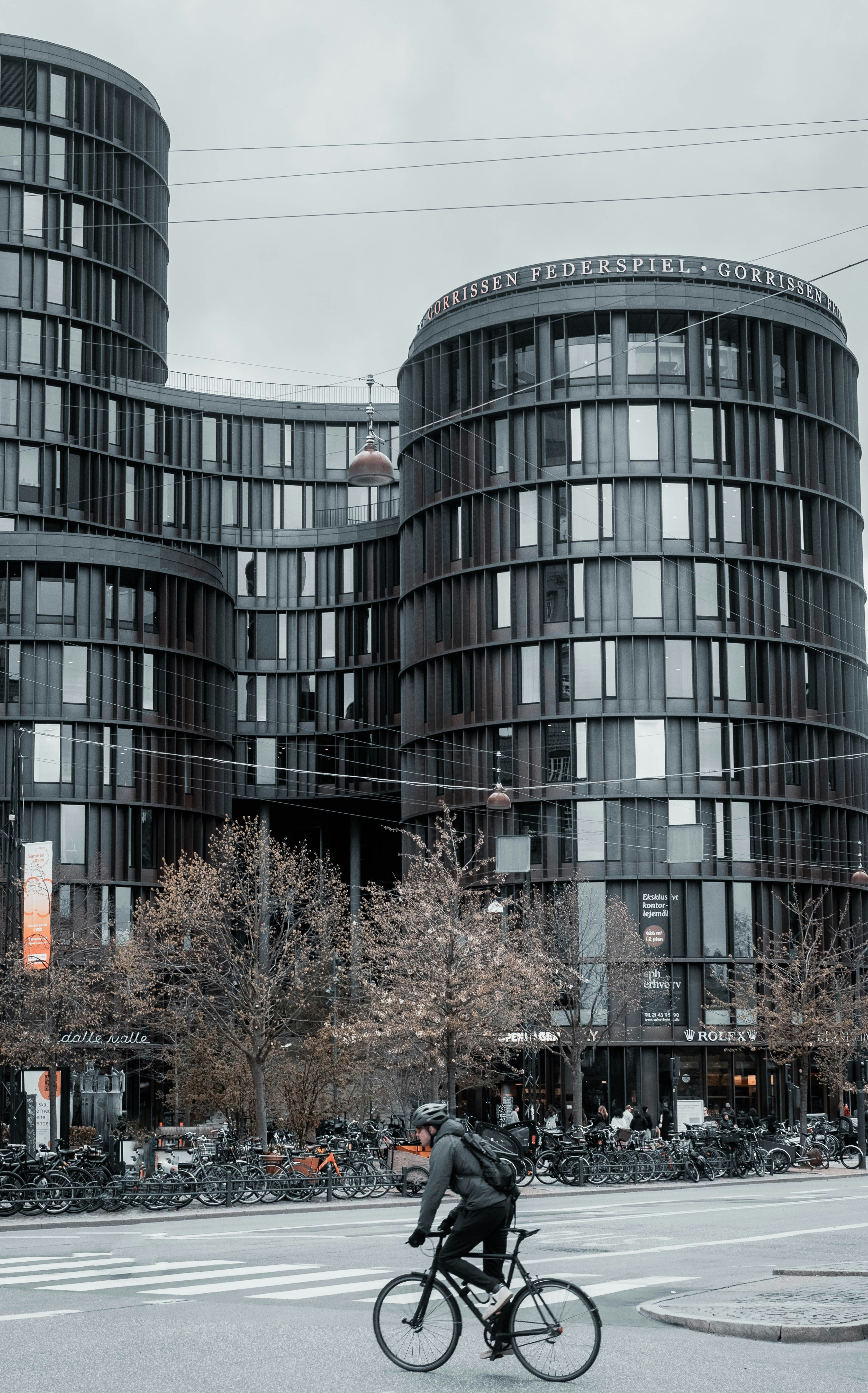 Cyclist in Front of Curved Glass Towers under Overcast Sky