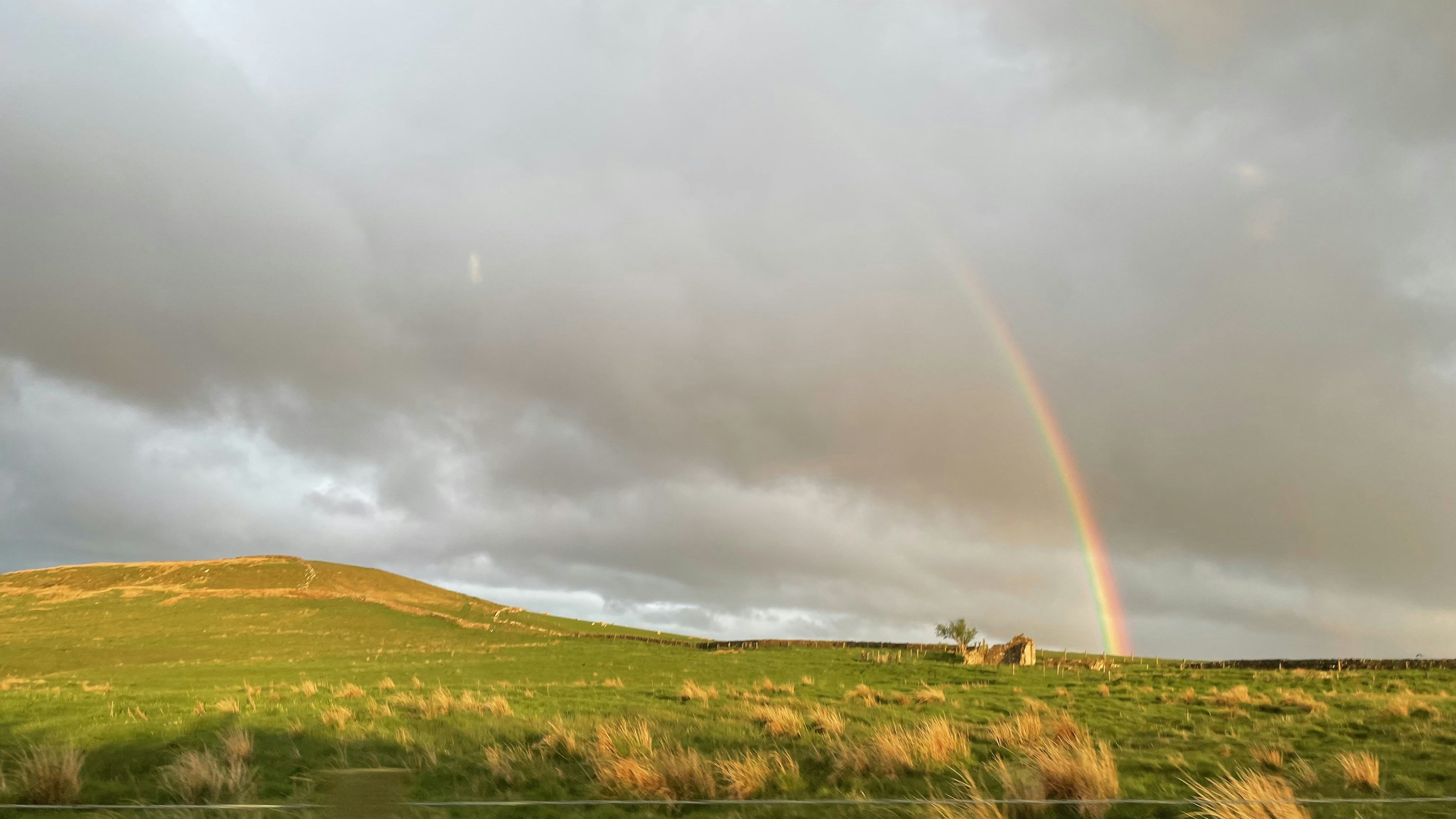 Arc in the Sky: A Lone Rainbow over Rolling Hills at Dusk
