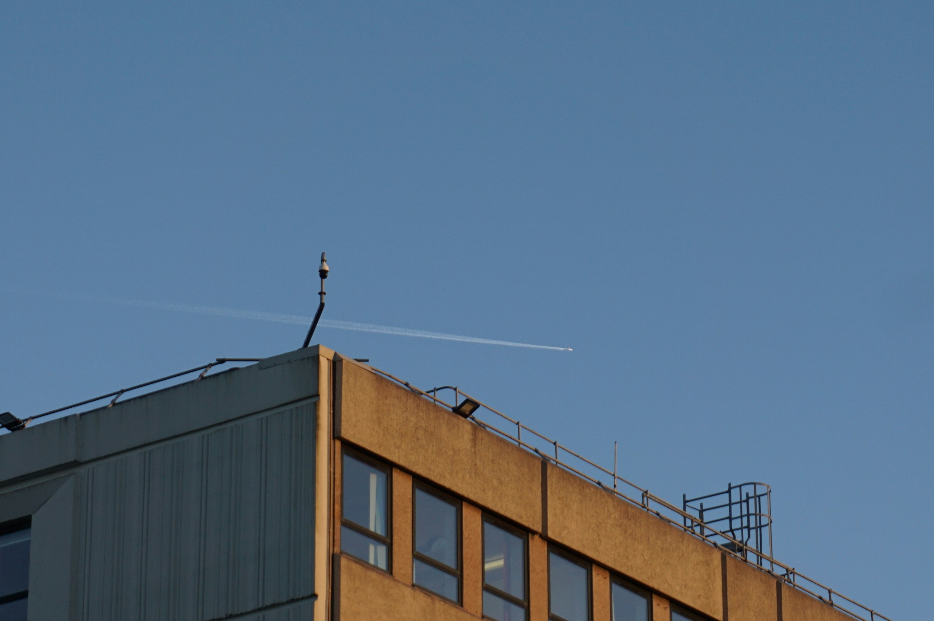 Edge of the Sky: Antenna on a Modern Roofline against a Clear Blue