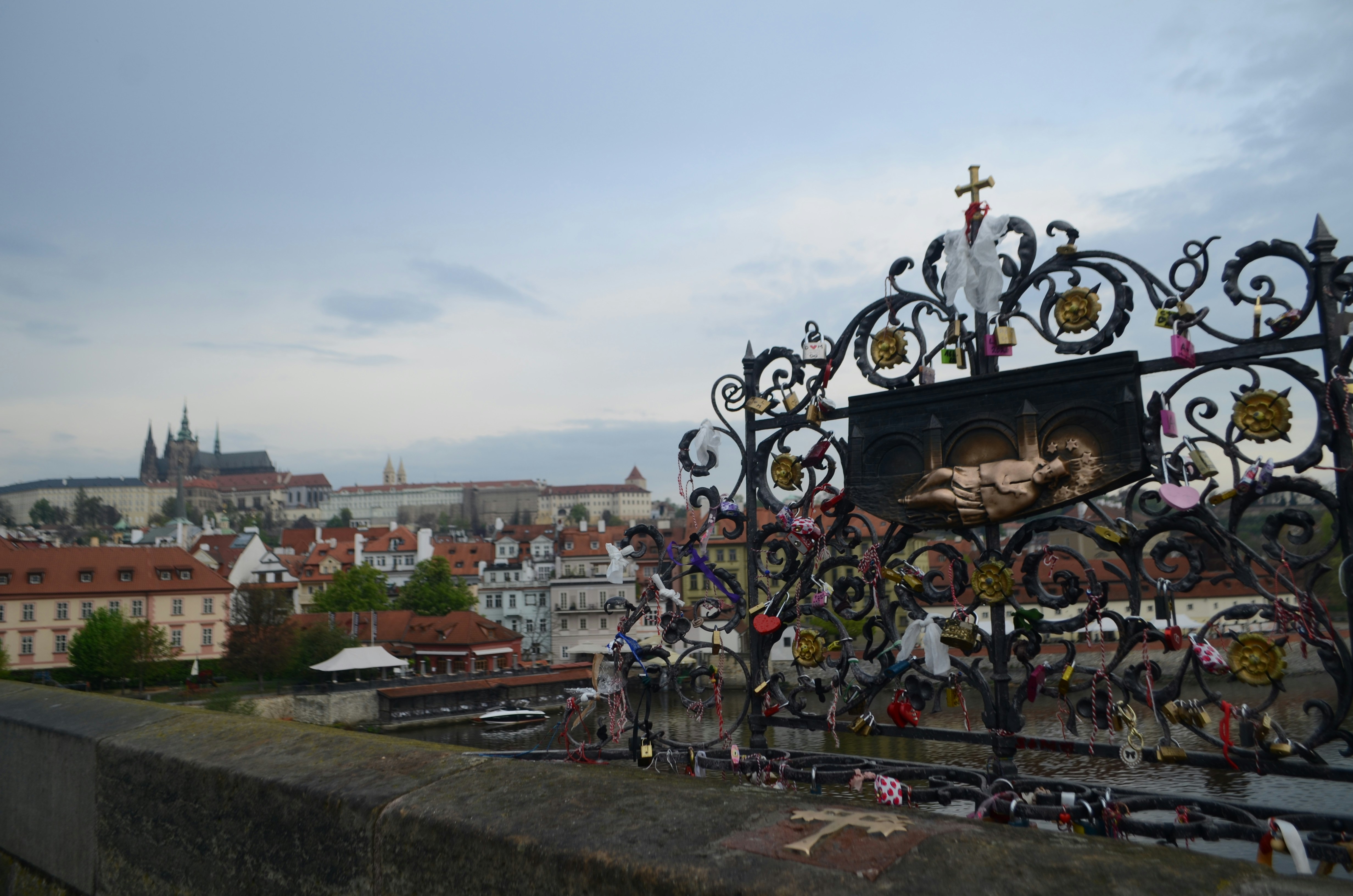 Vignette of a decorative shrine on a bridge foreground with a distant European cityscape and river in the background.