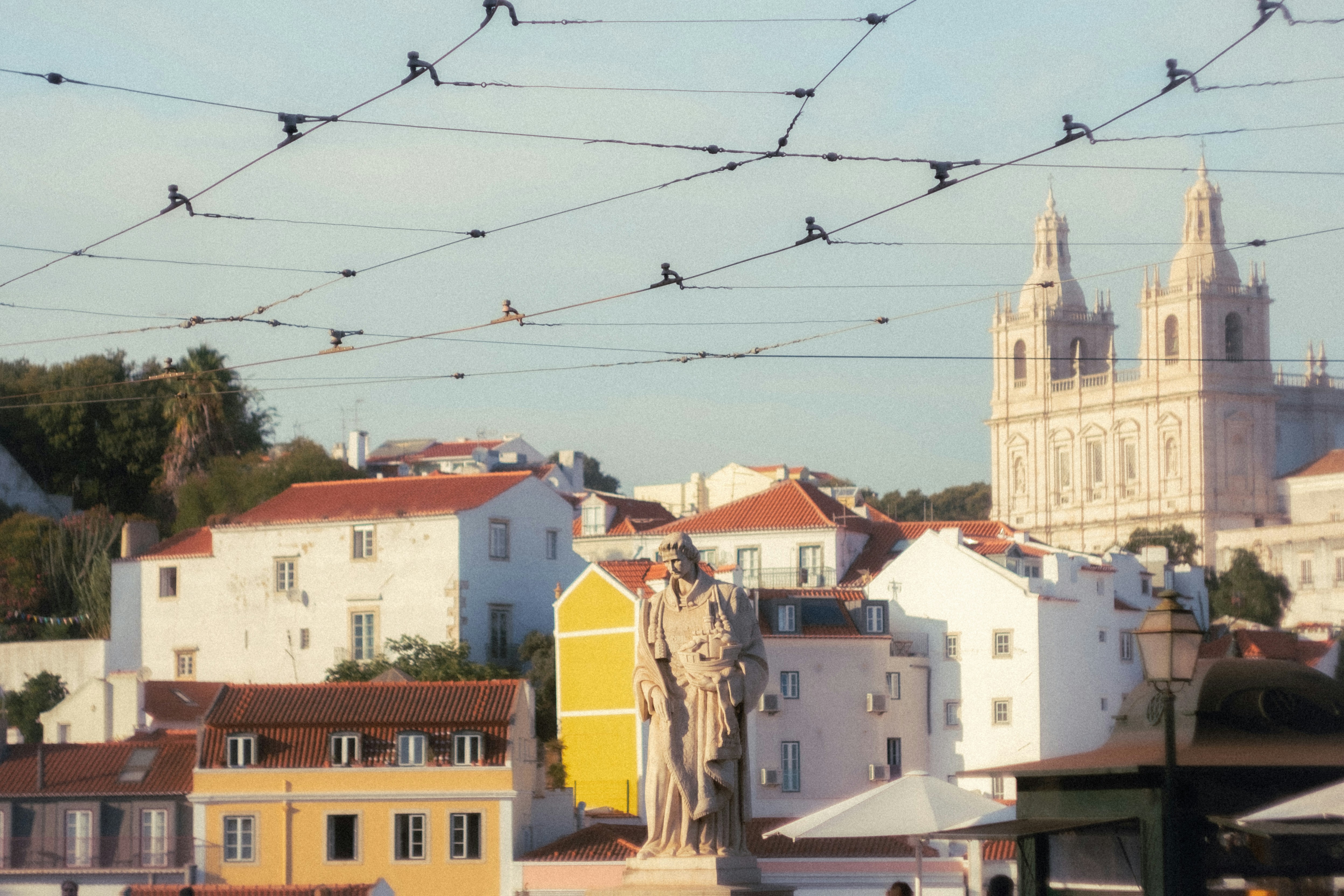 Statue-lined plaza with distant cathedral towers under a web of overhead wires