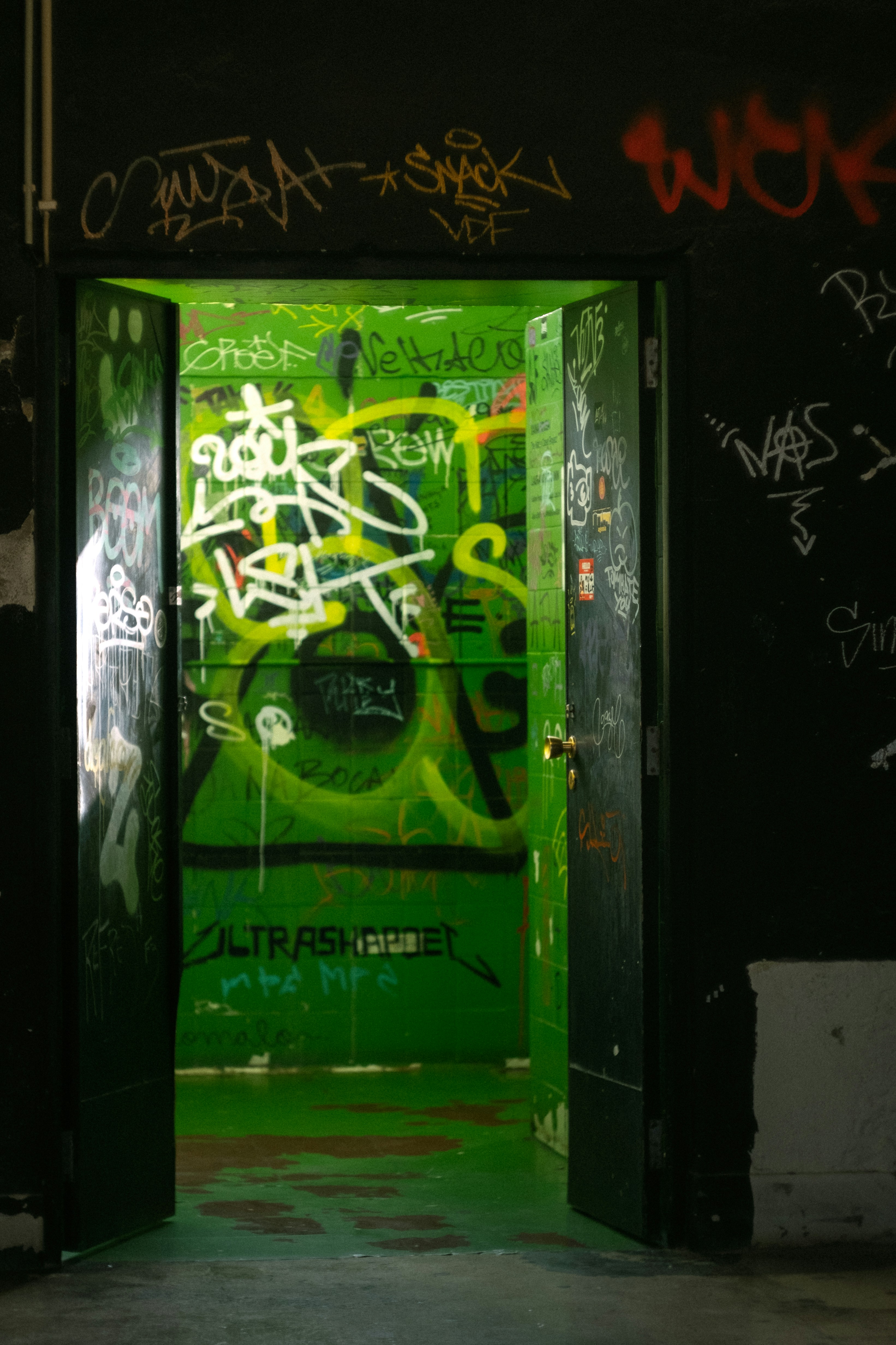 Graffiti-Splashed Vault: Neon Green Portal Through Open Doors