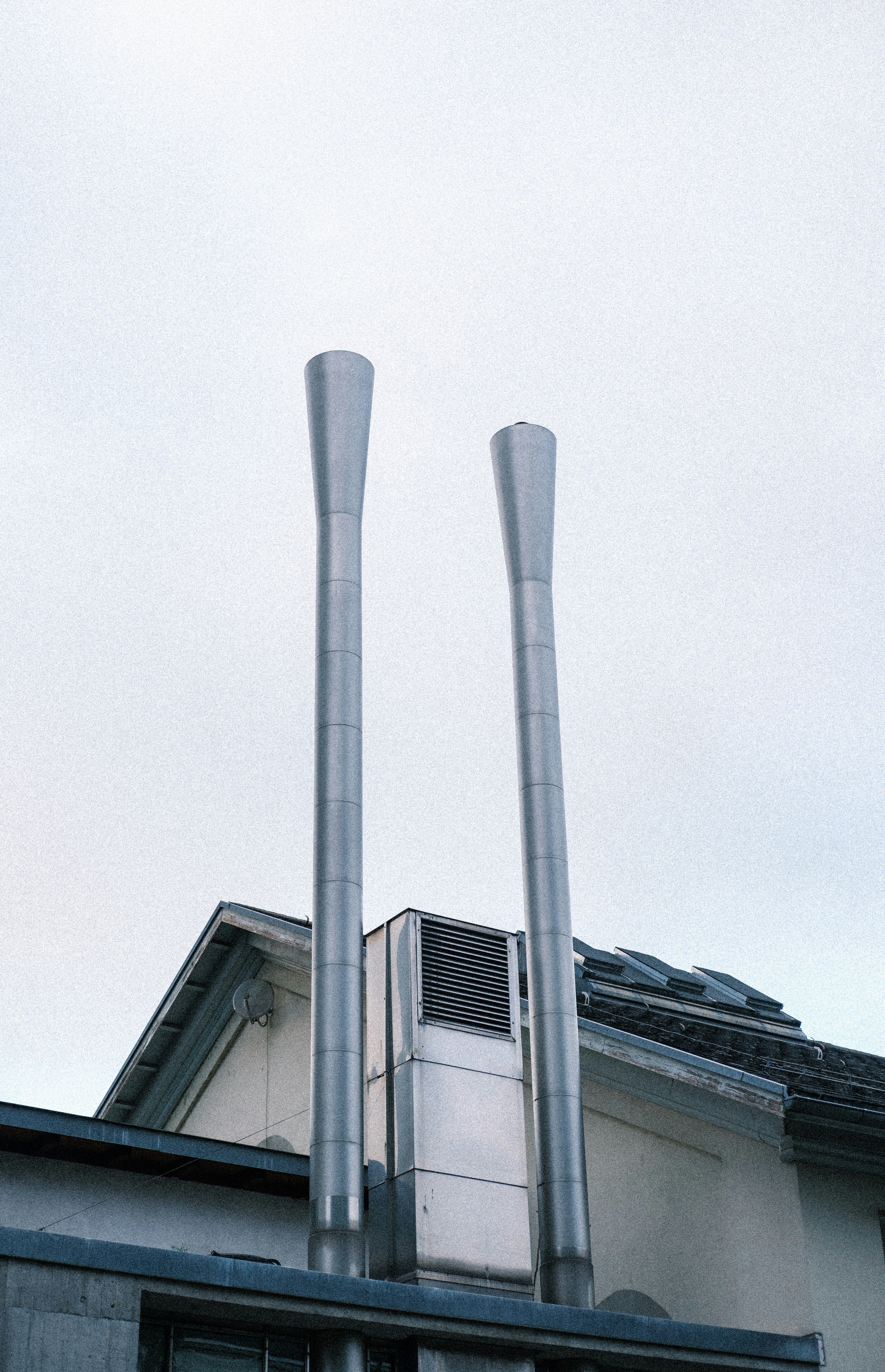 Industrial chimneys rise above a quiet rooftop under pale light