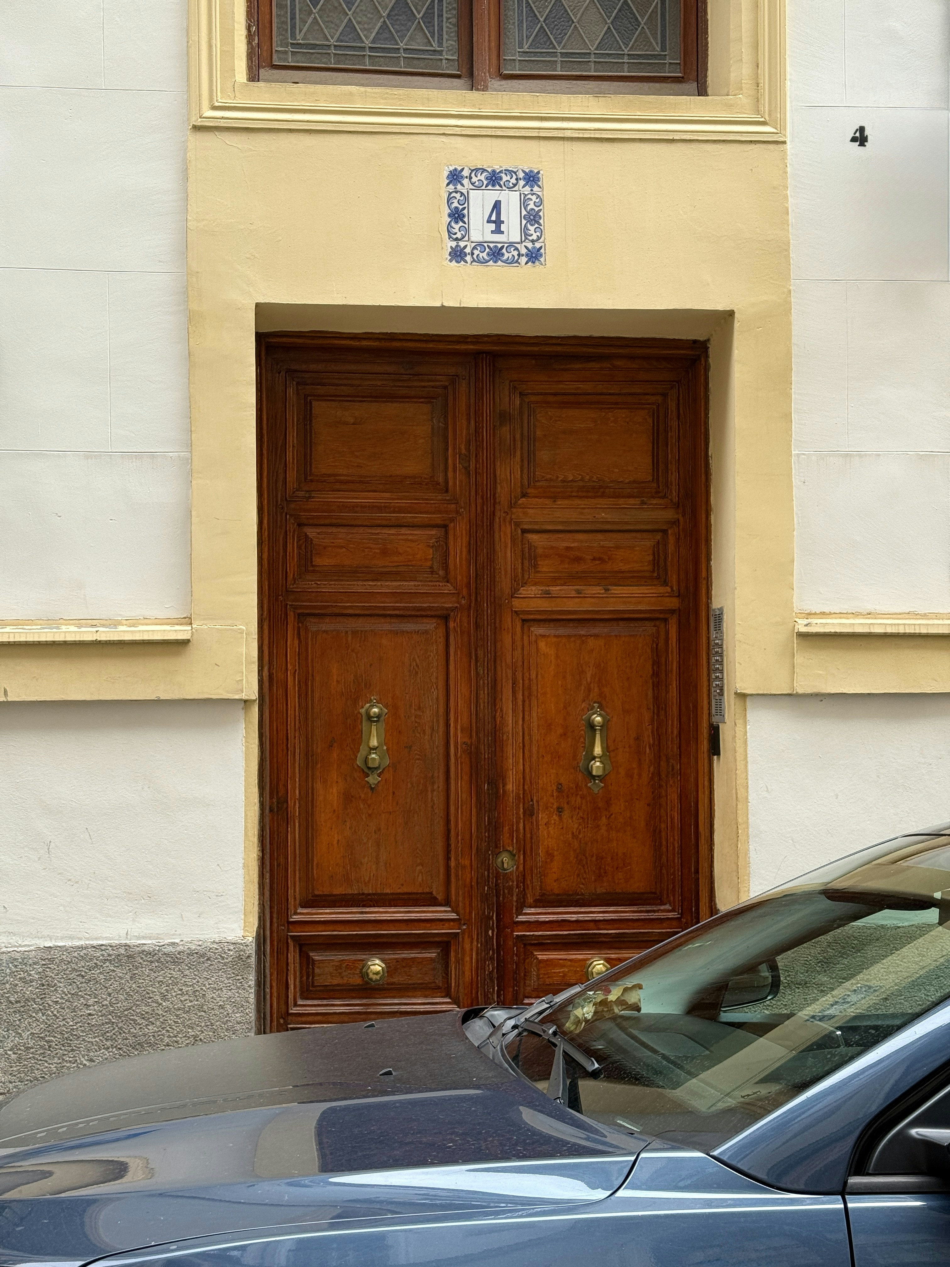 Weathered door with brass handles under a blue-and-white tile plaque