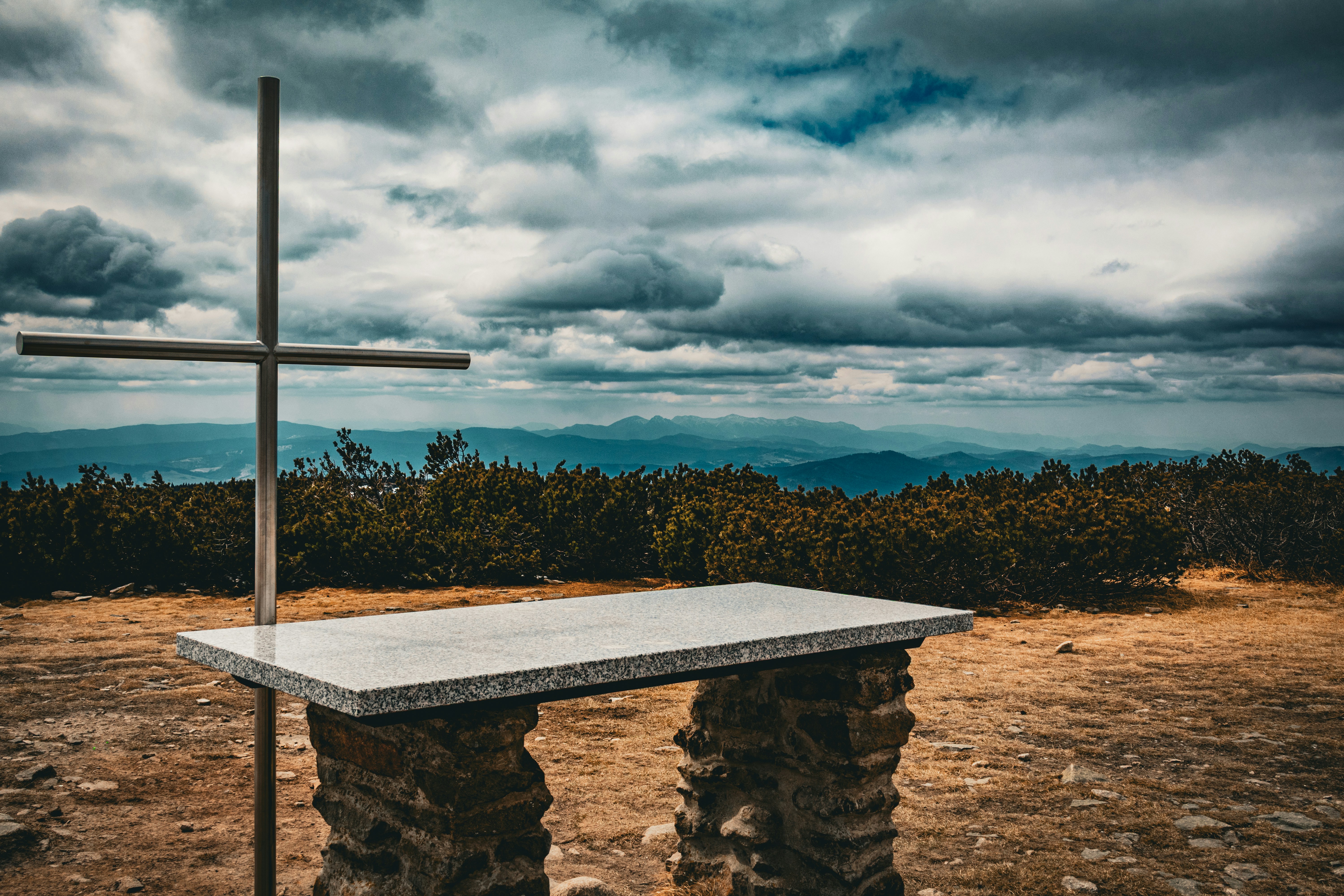 Cross on a hilltop: weathered stone table with distant ridge