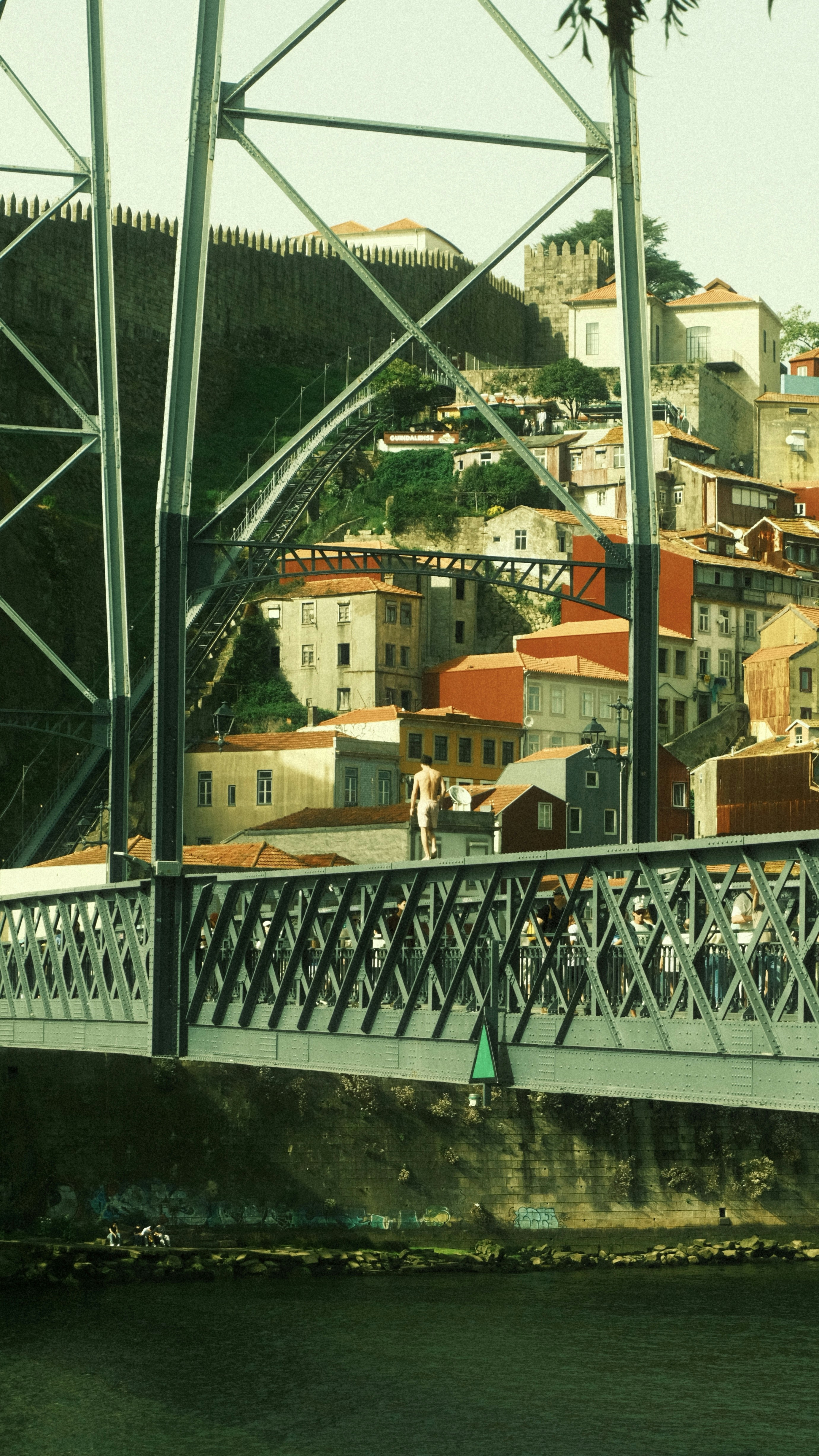Riveted Span: A solitary figure on a steel bridge above a tiled hillside town