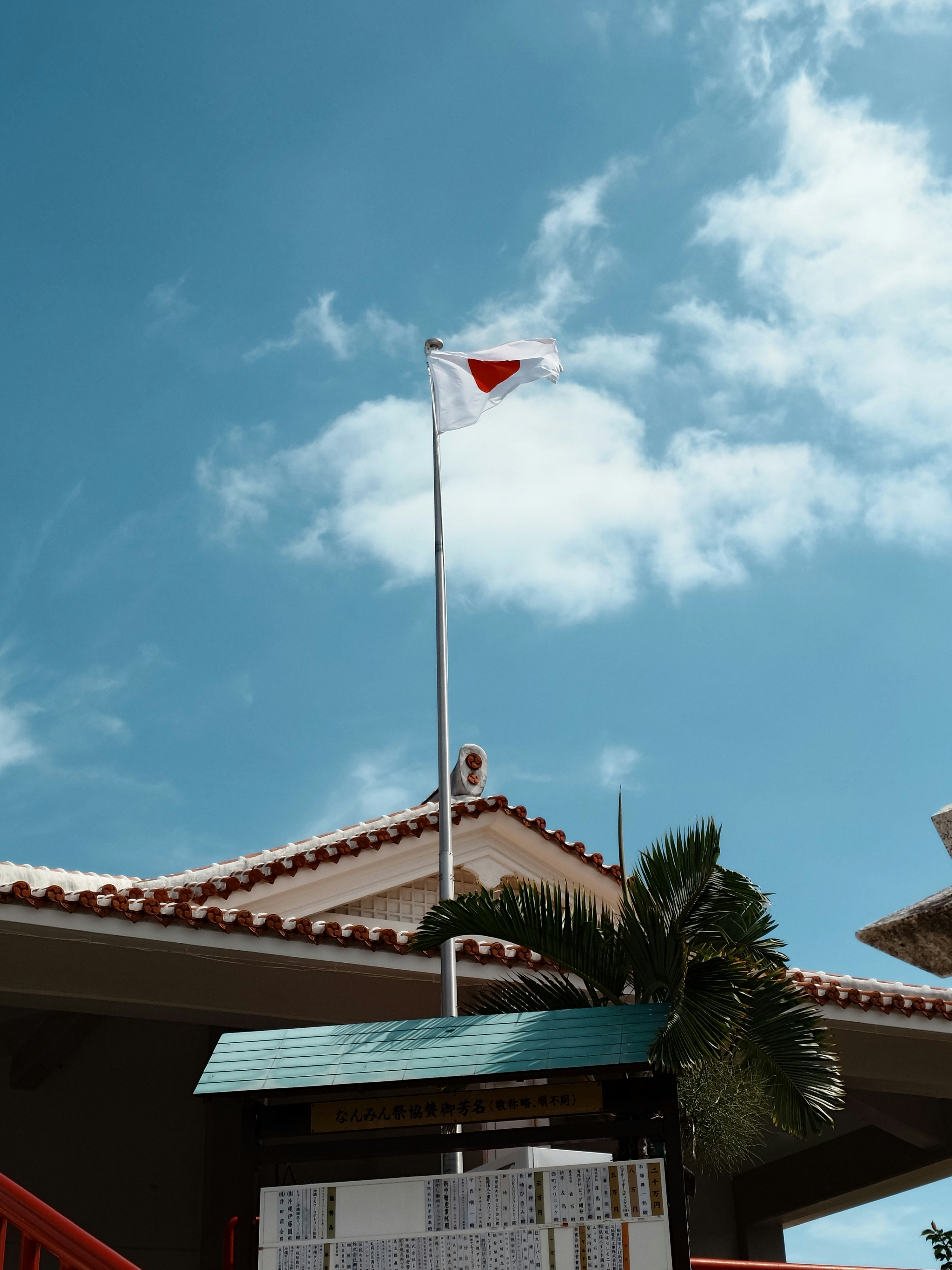 Flagpole under a clear blue sky over a tiled roof