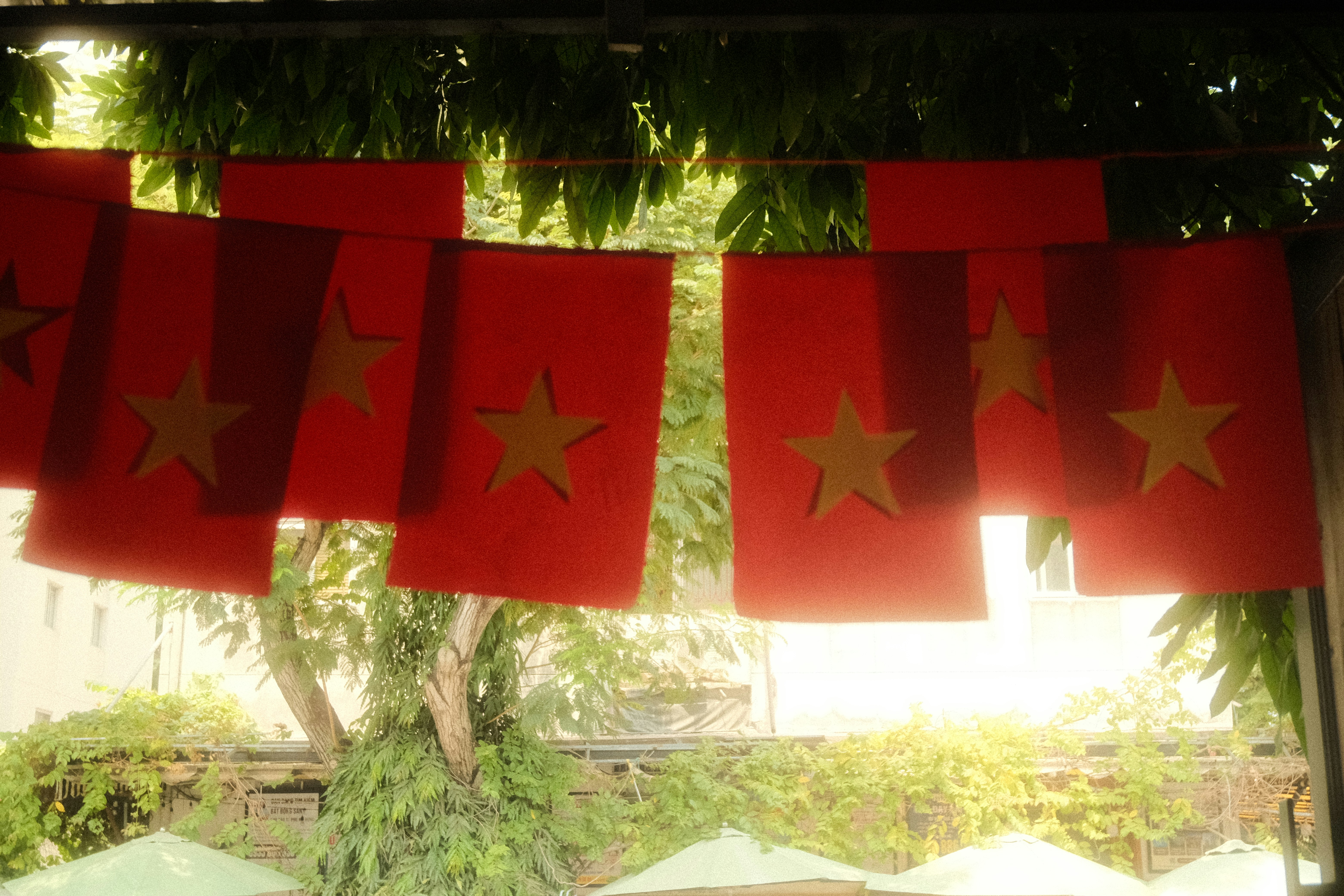 Rows of red flags with gold stars flutter in a sunlit courtyard