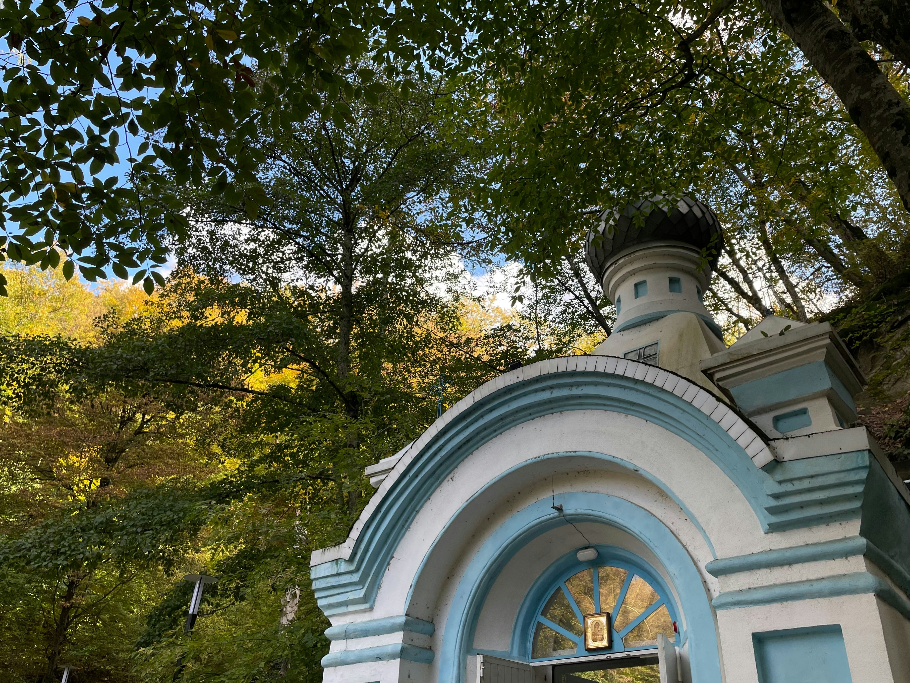 Blue-arched caretaker: a sunlit pavilion rises among autumn foliage