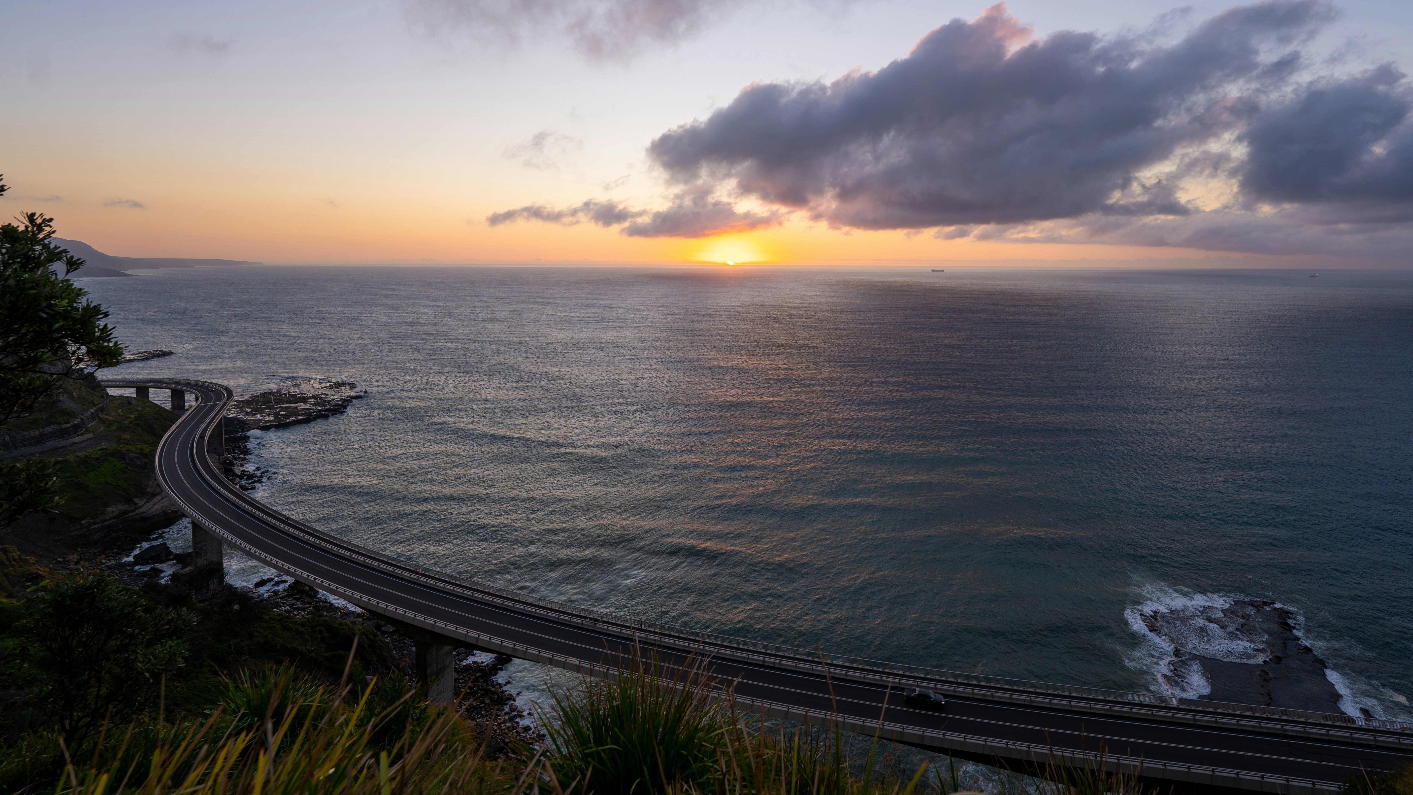 Coastal highway curves along the ocean at sunset.