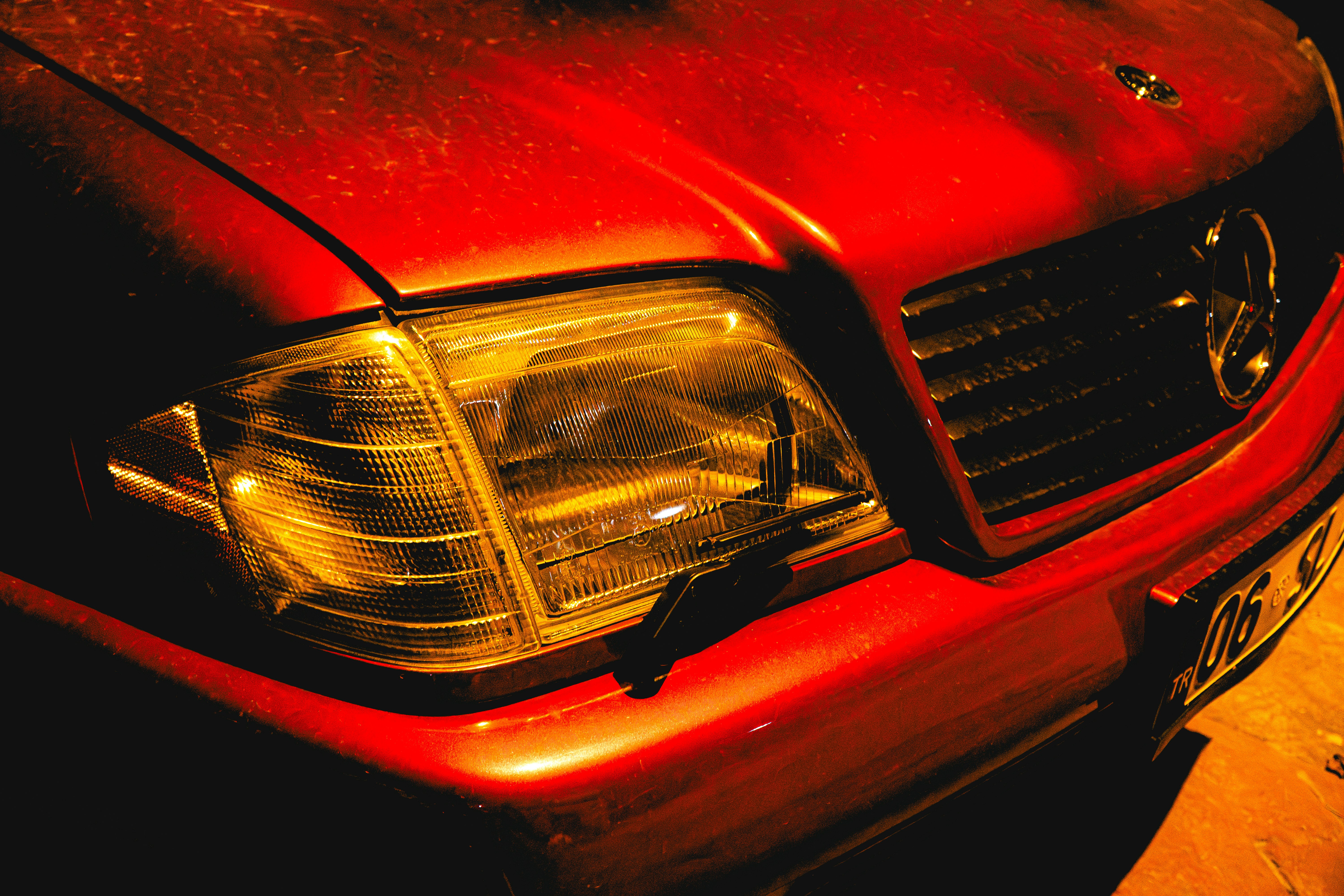 Close-up of a red vintage Mercedes front detail under warm streetlight