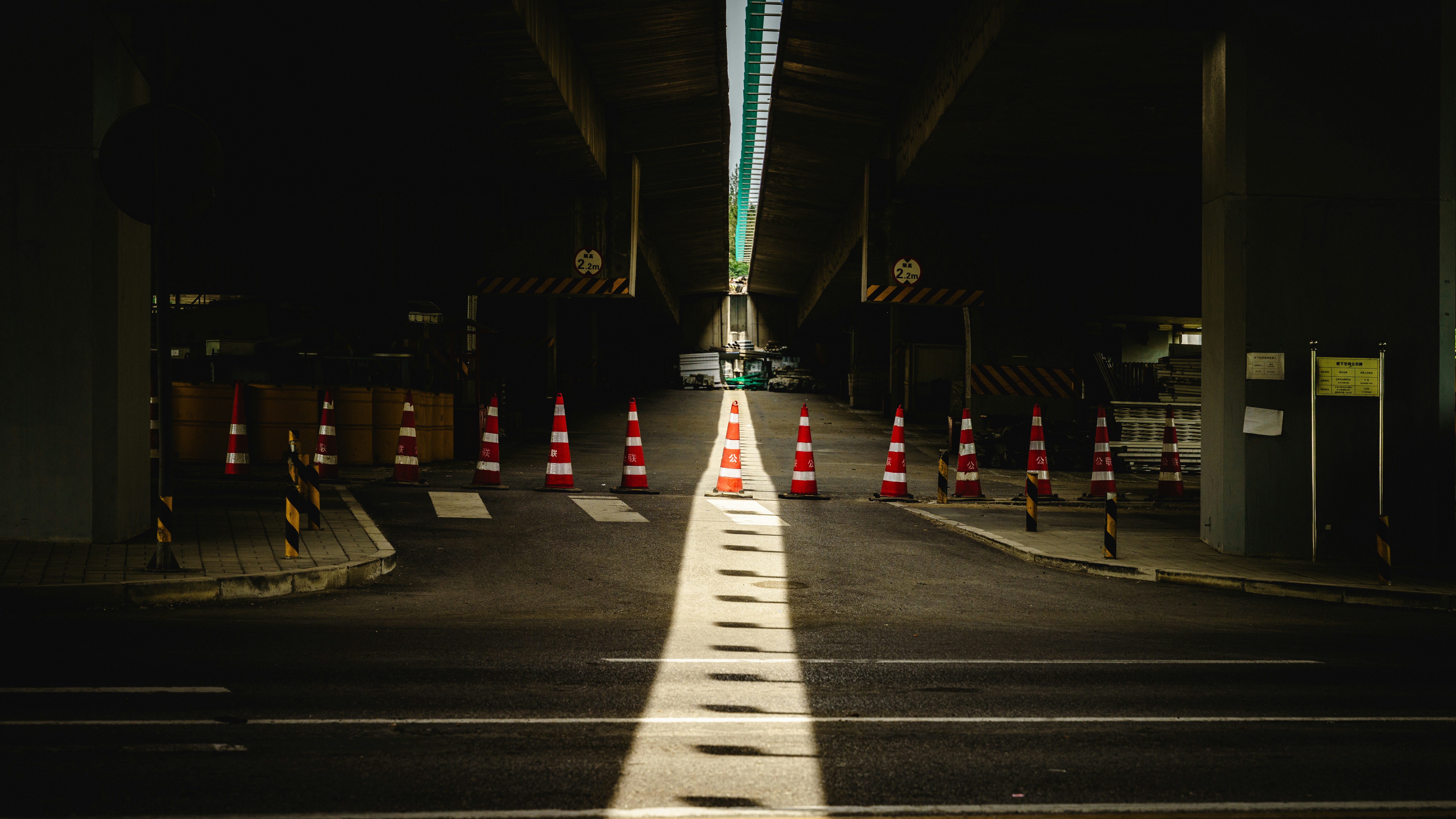A dark road with traffic cones under an overpass.