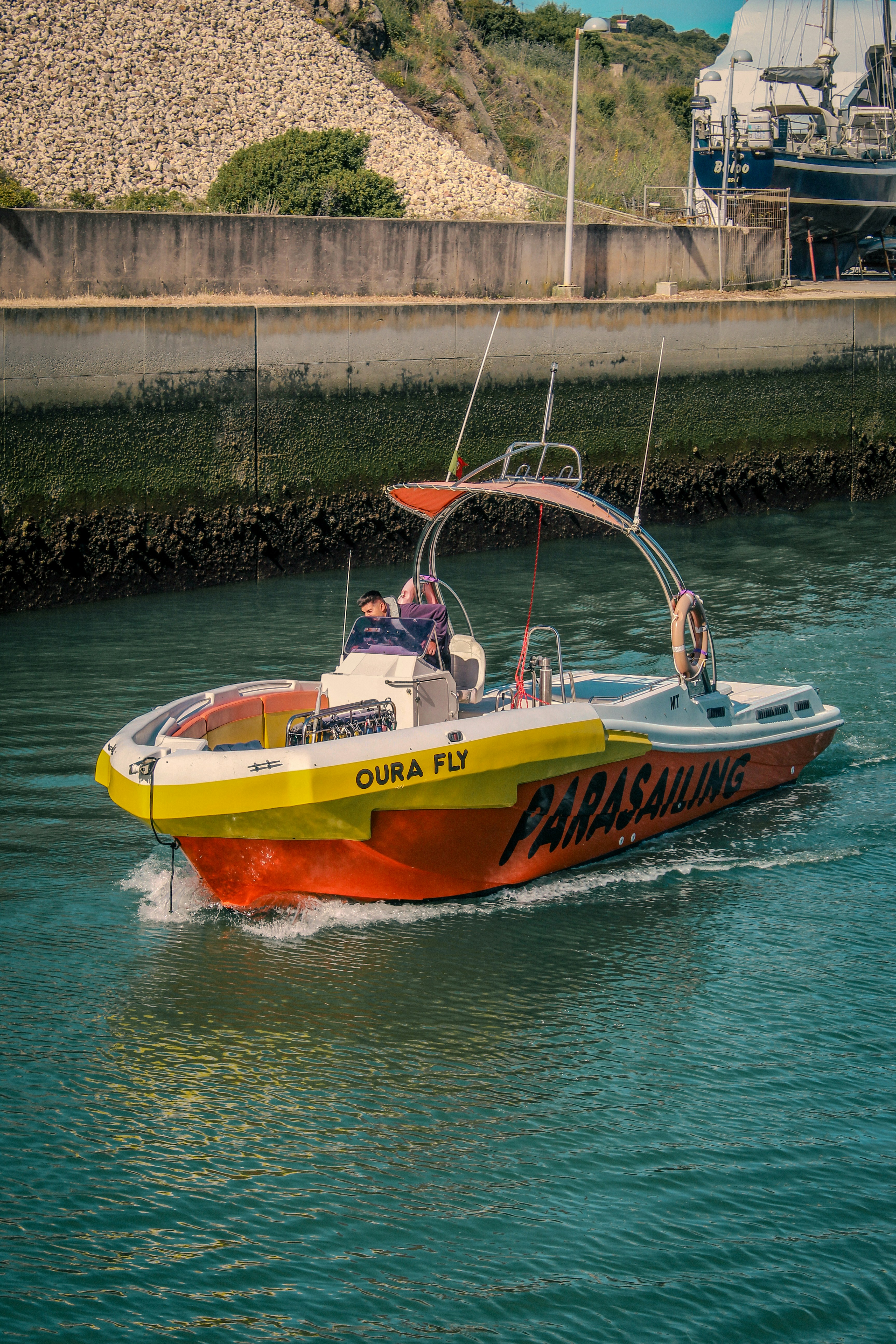 Vibrant parasailing boat glides through turquoise harbor with bold yellow and red hulls and a clear dock backdrop.