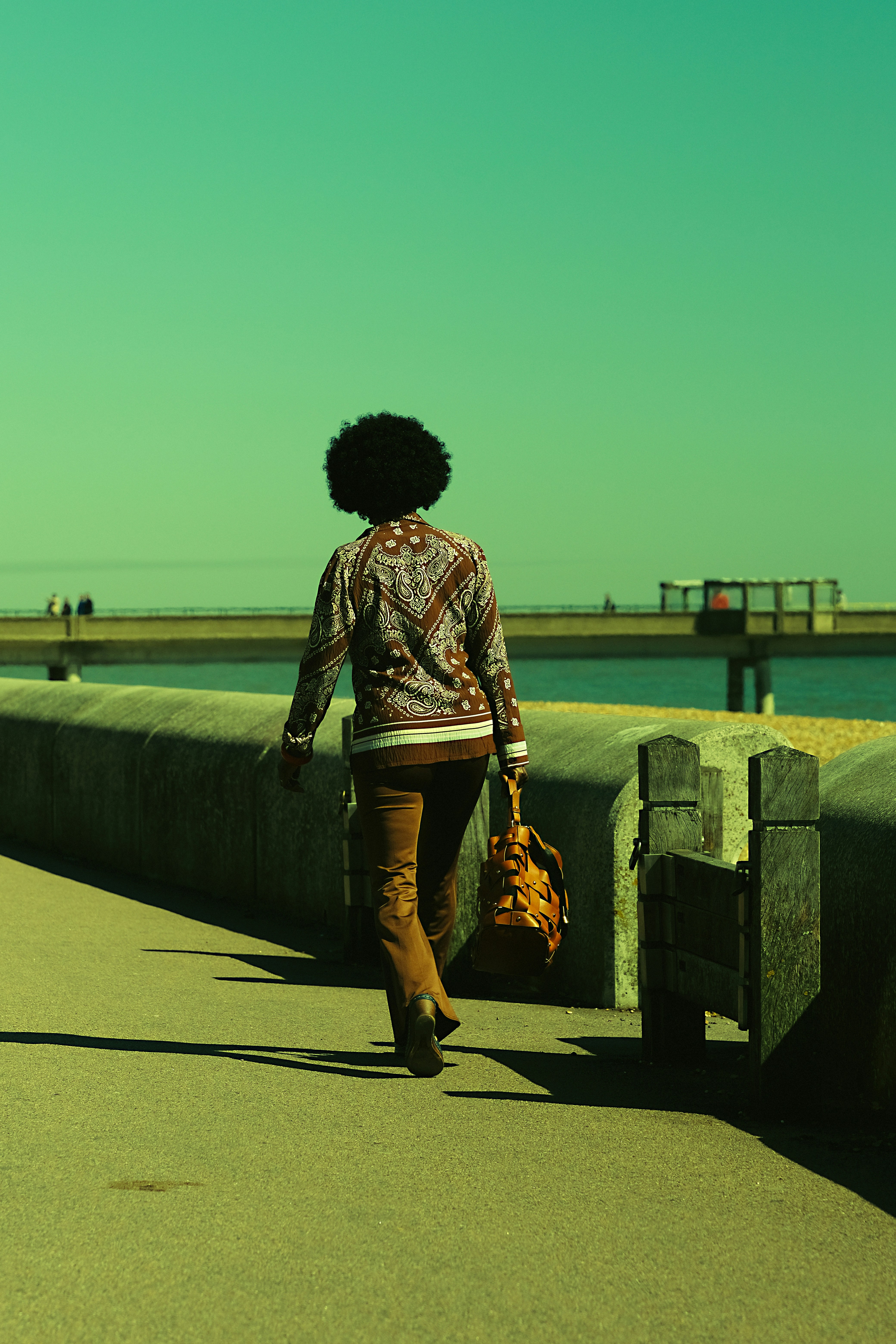 The Walkway Portrait: A Figure with Afro and Leather Bag heads toward the Pier