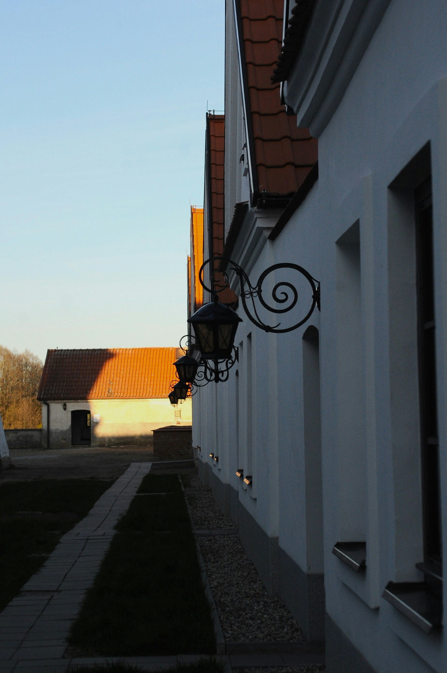 Sunlit eaves and ornamental lamps along a white-washed wall