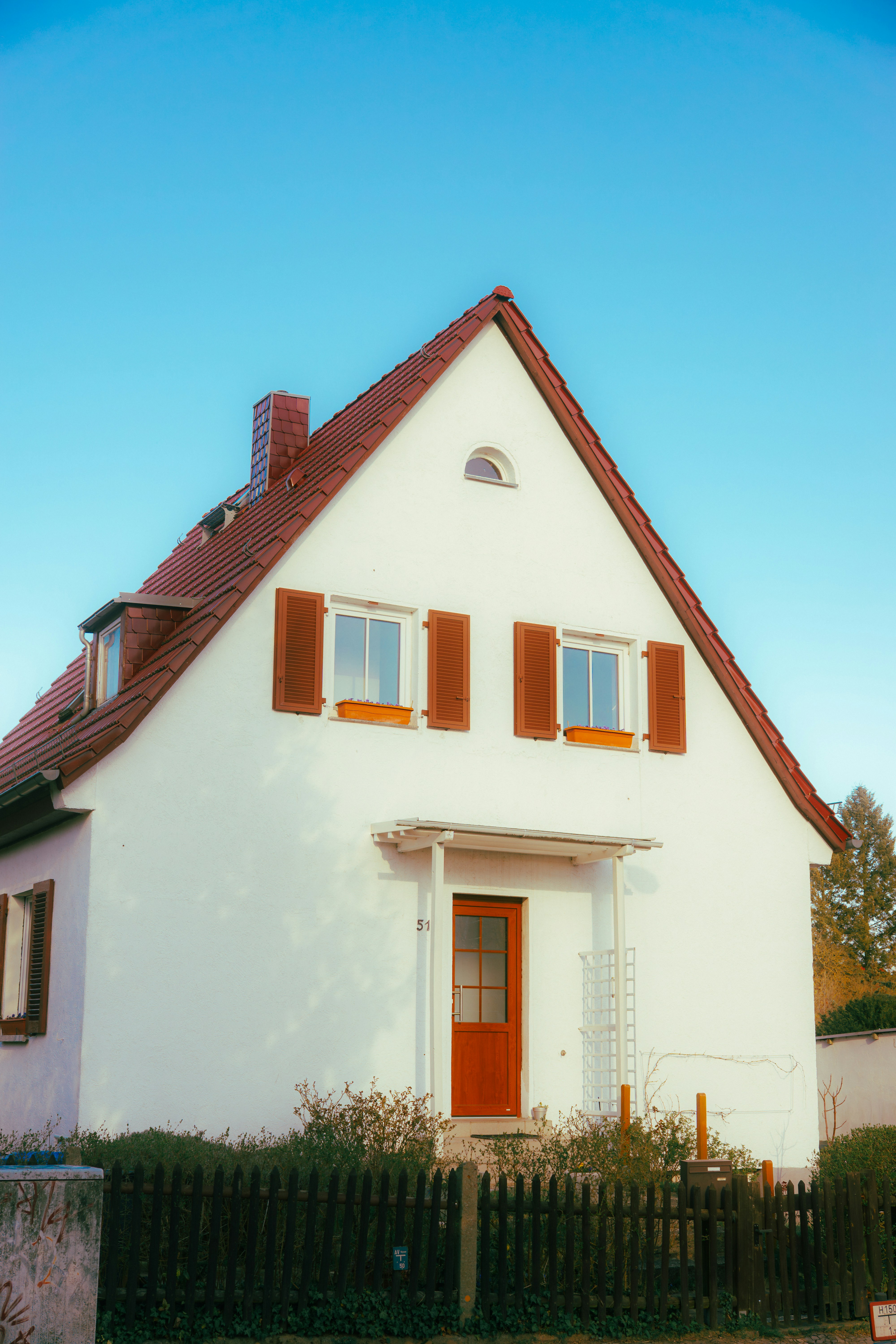 Sunlit A-frame House with Red-Tiled Roof and Shuttered Windows