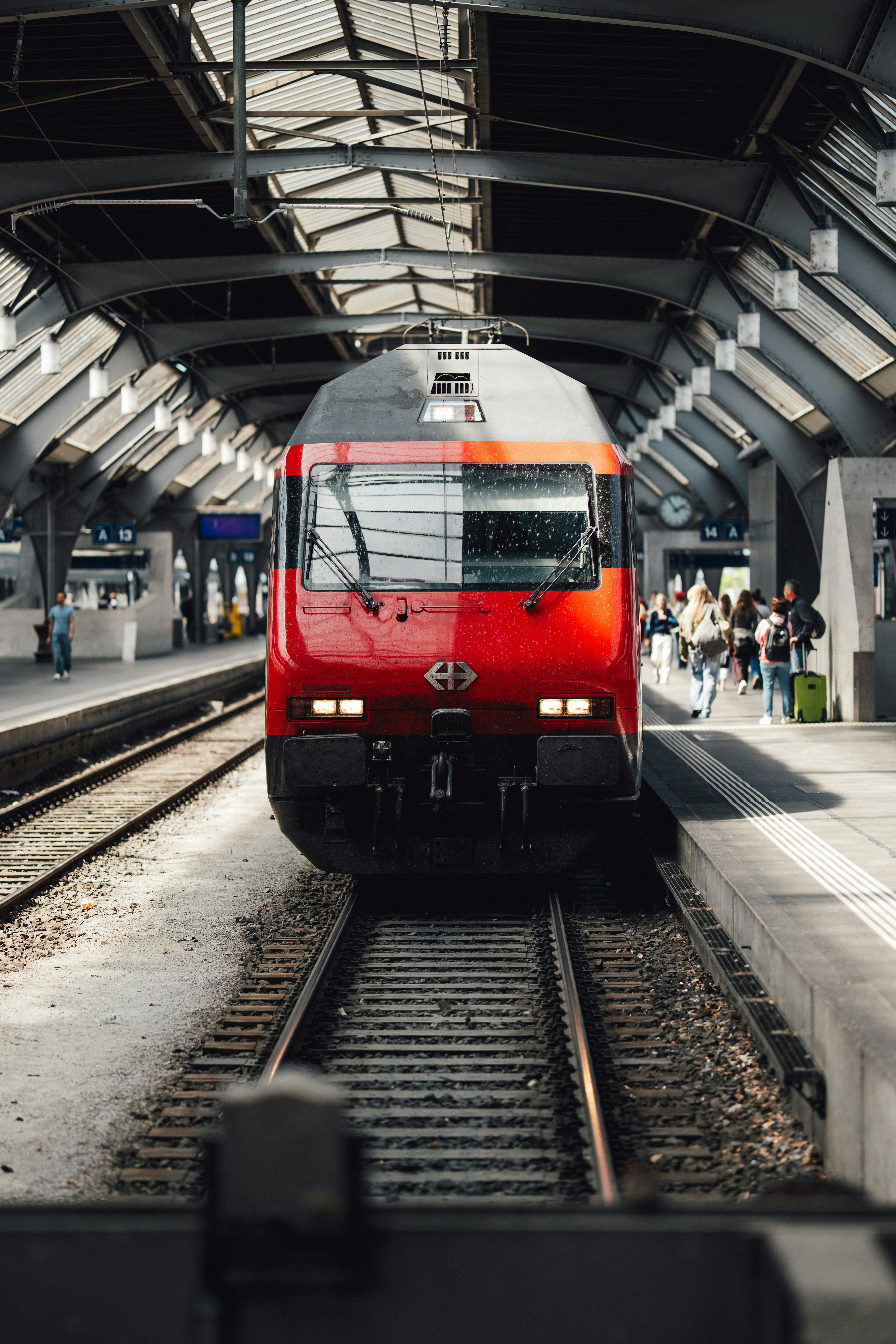 Red locomotive at a sunlit metro platform framed by steel arches