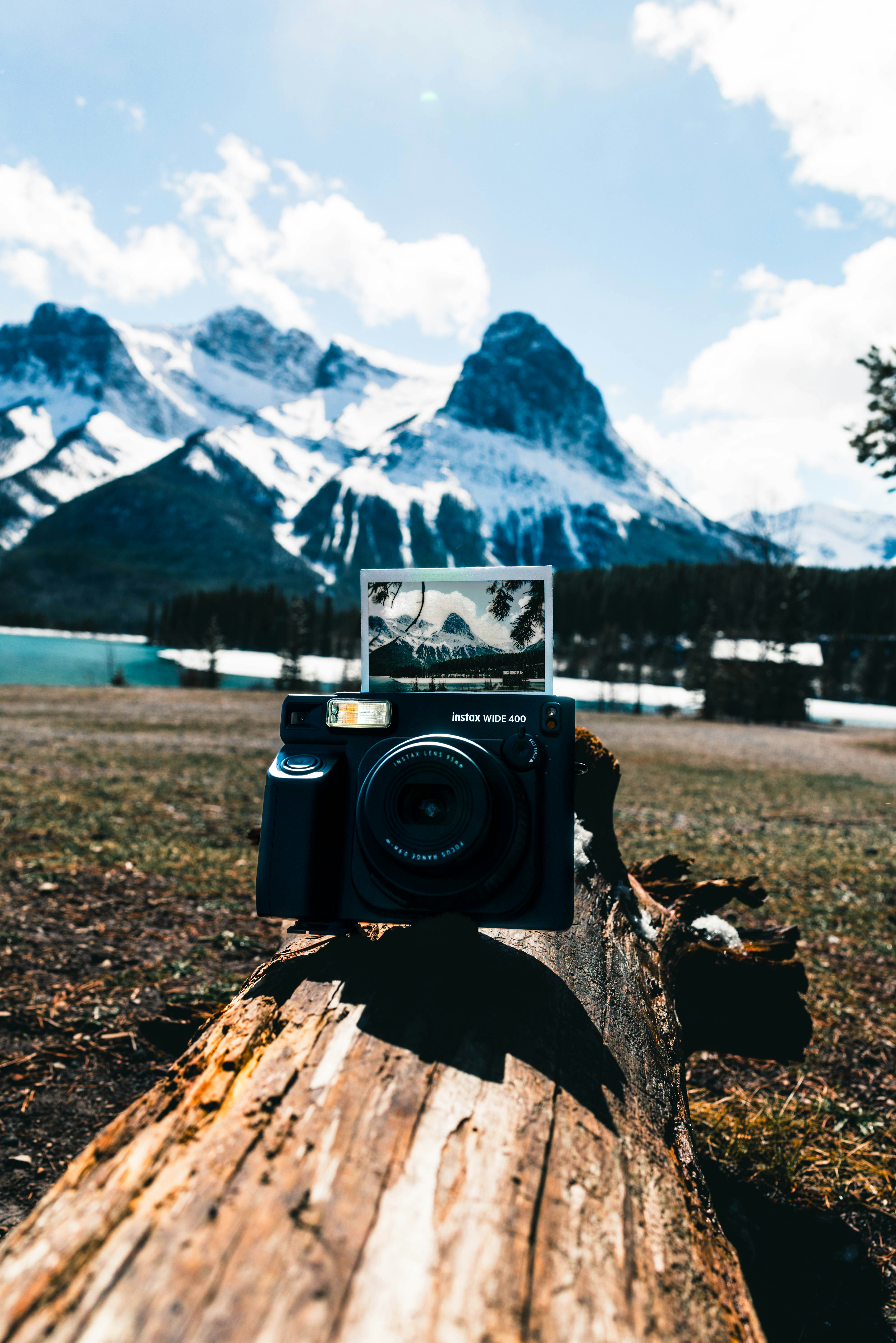 Polaroid Pause: A Camera on a Weathered Log Before Snow-Capped Peaks