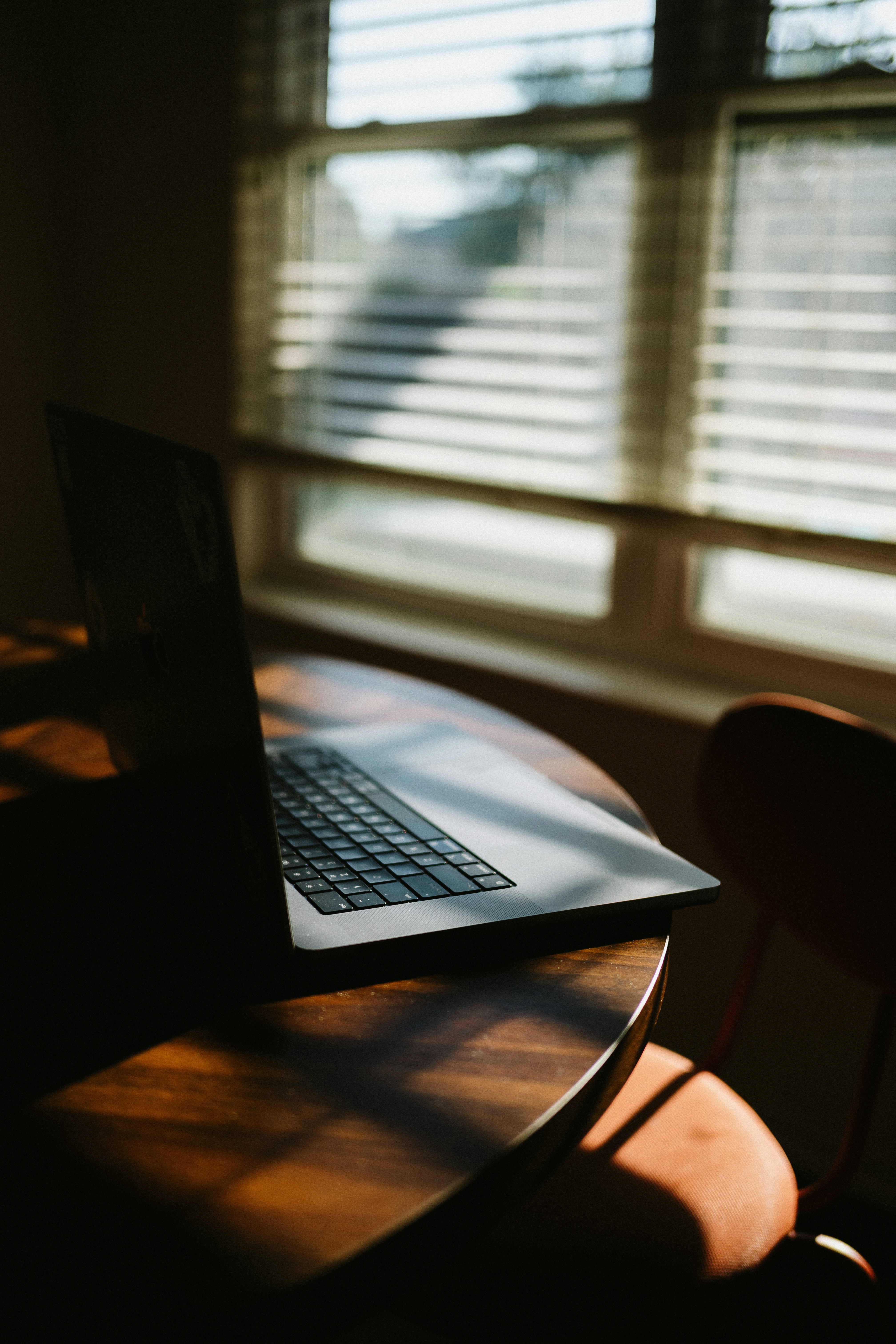 Sunlit Quiet: A Laptop Bathed in Window Light on a Round Table