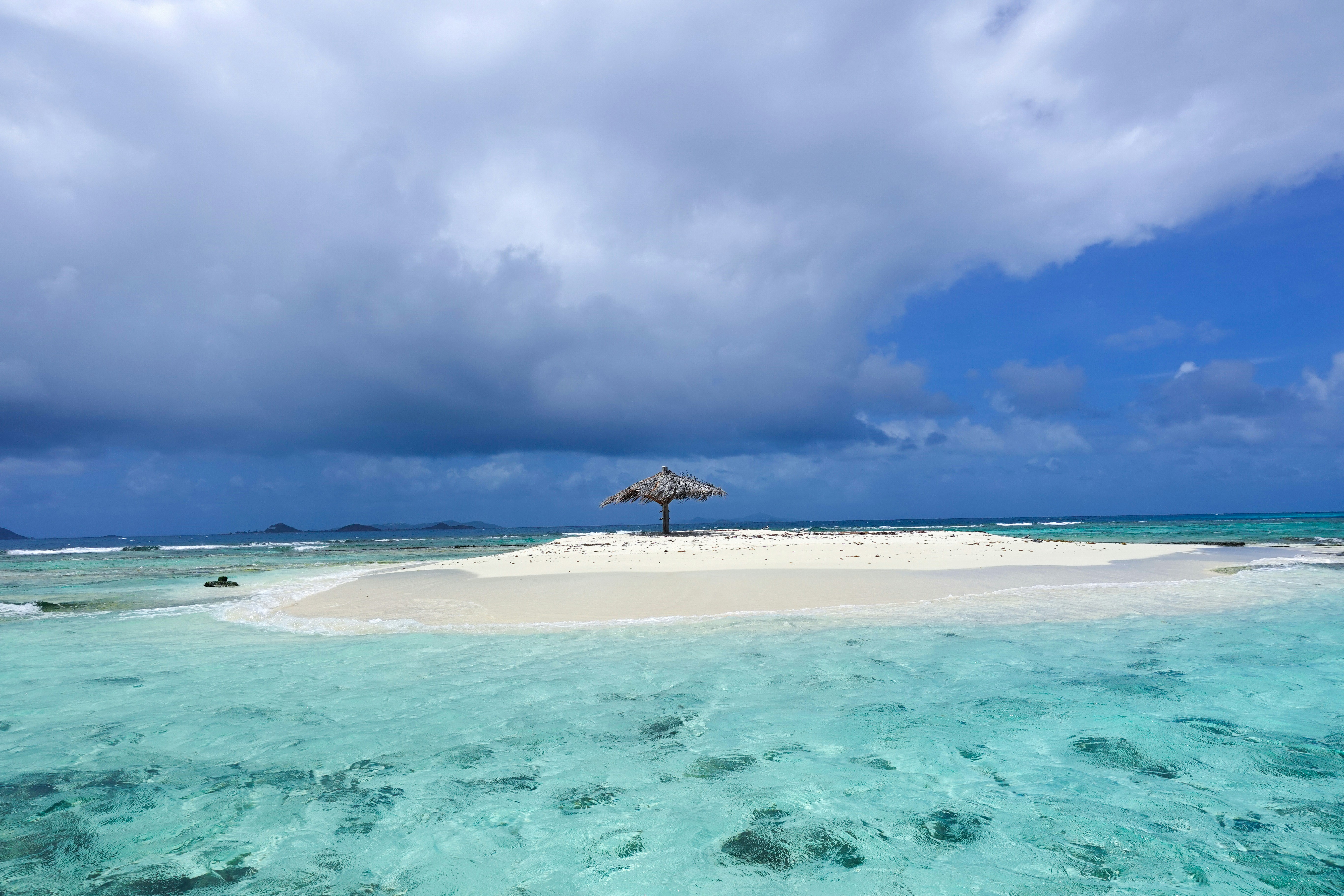 Small tropical island with a thatched umbrella and clear water.