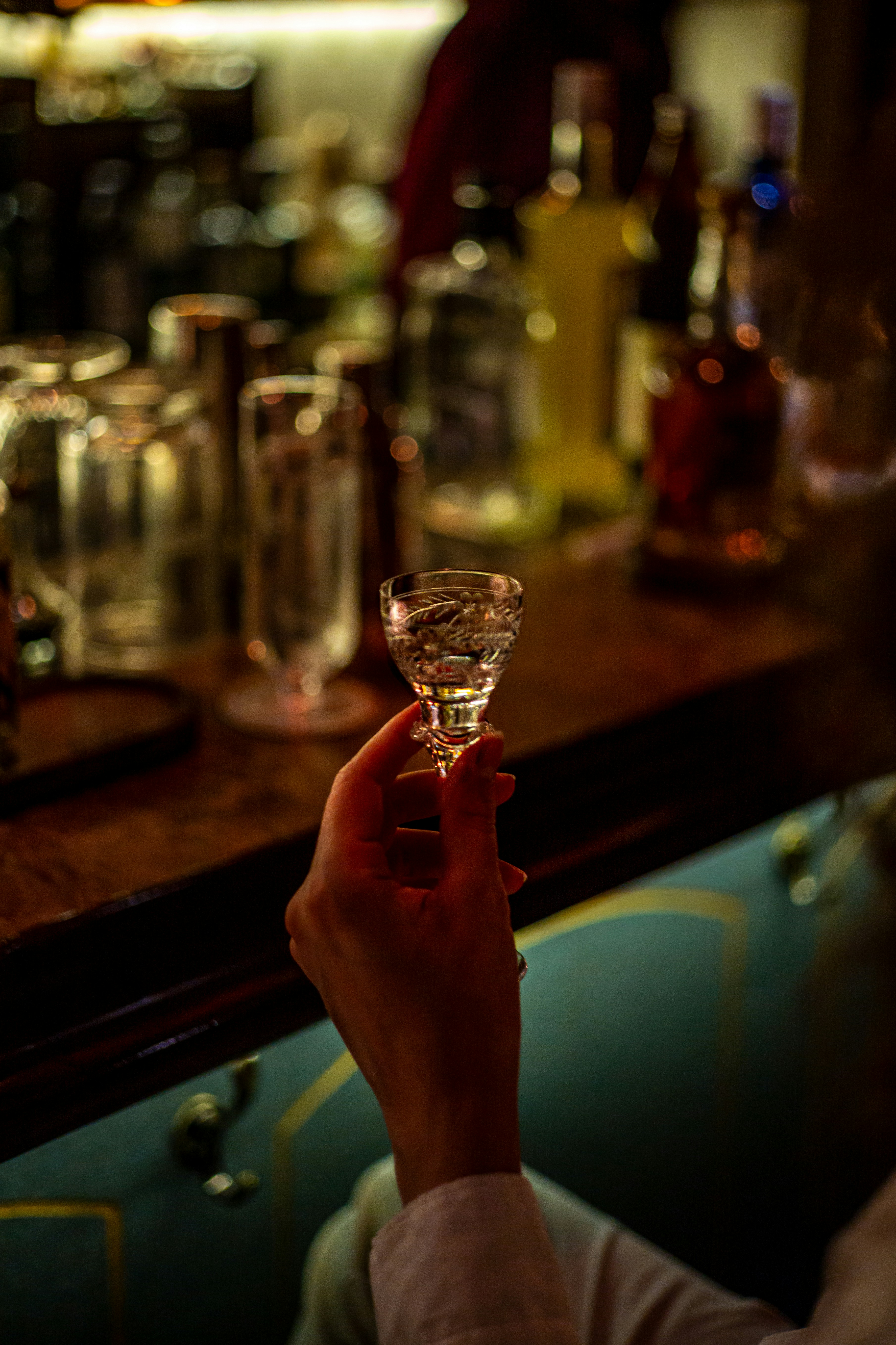 Glimmering Toast: A Hand Elevates a Crystal Glass in a Dim Bar