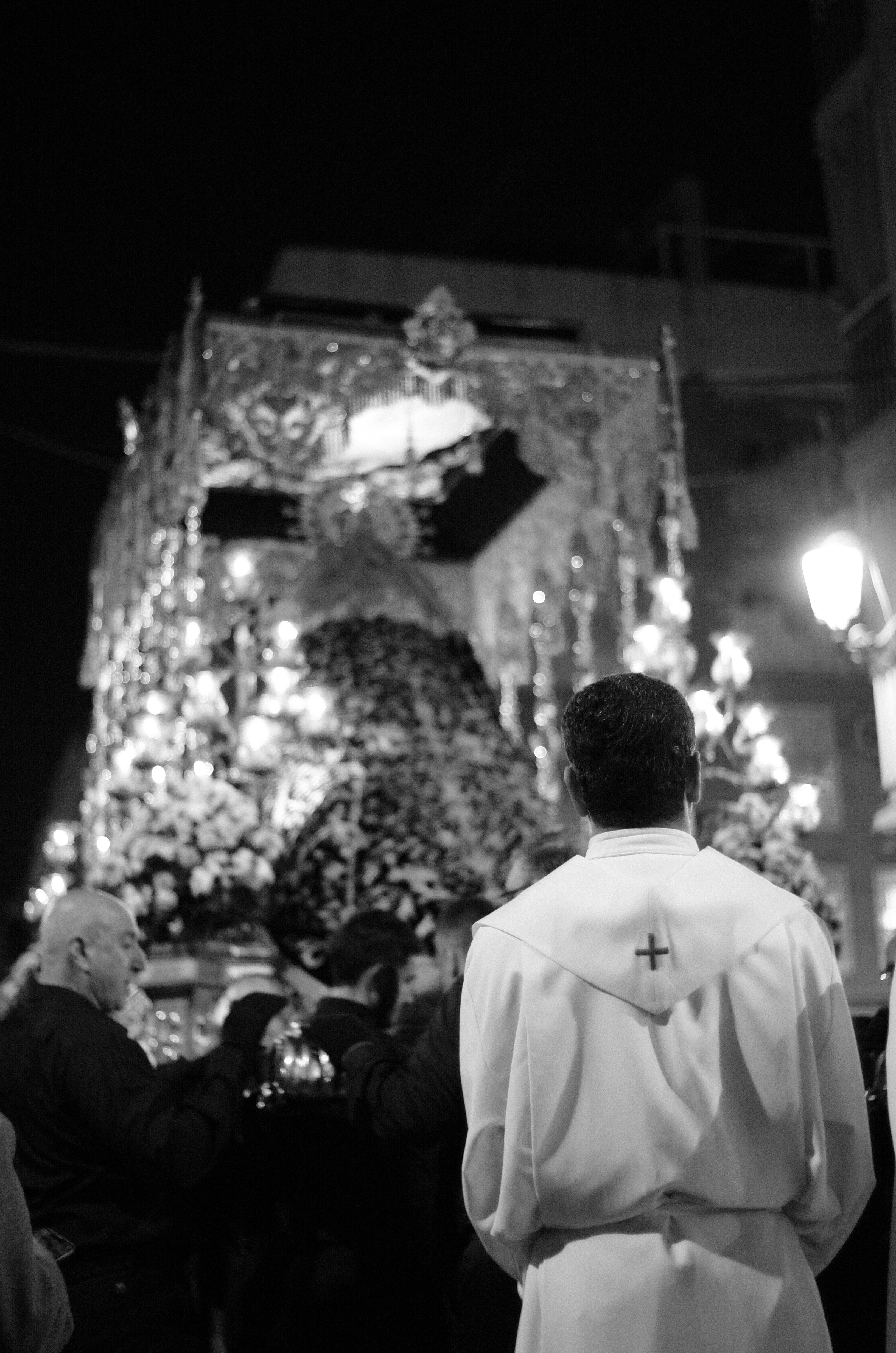 Quiet Cleric in the Night Procession Beneath a Floral Carriage