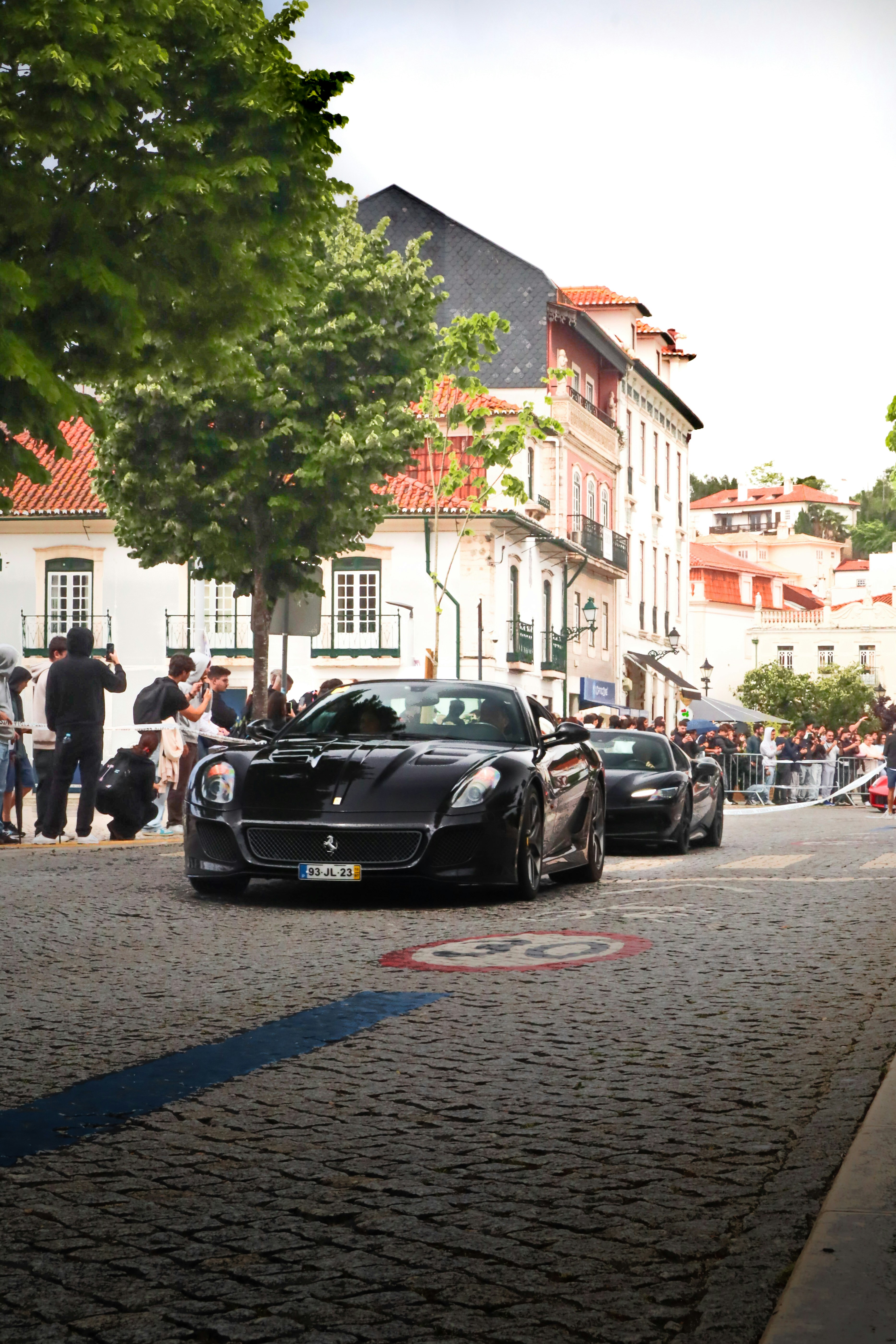 Black Ferrari Leads a Cobblestone Parade Through a Sunlit European Street