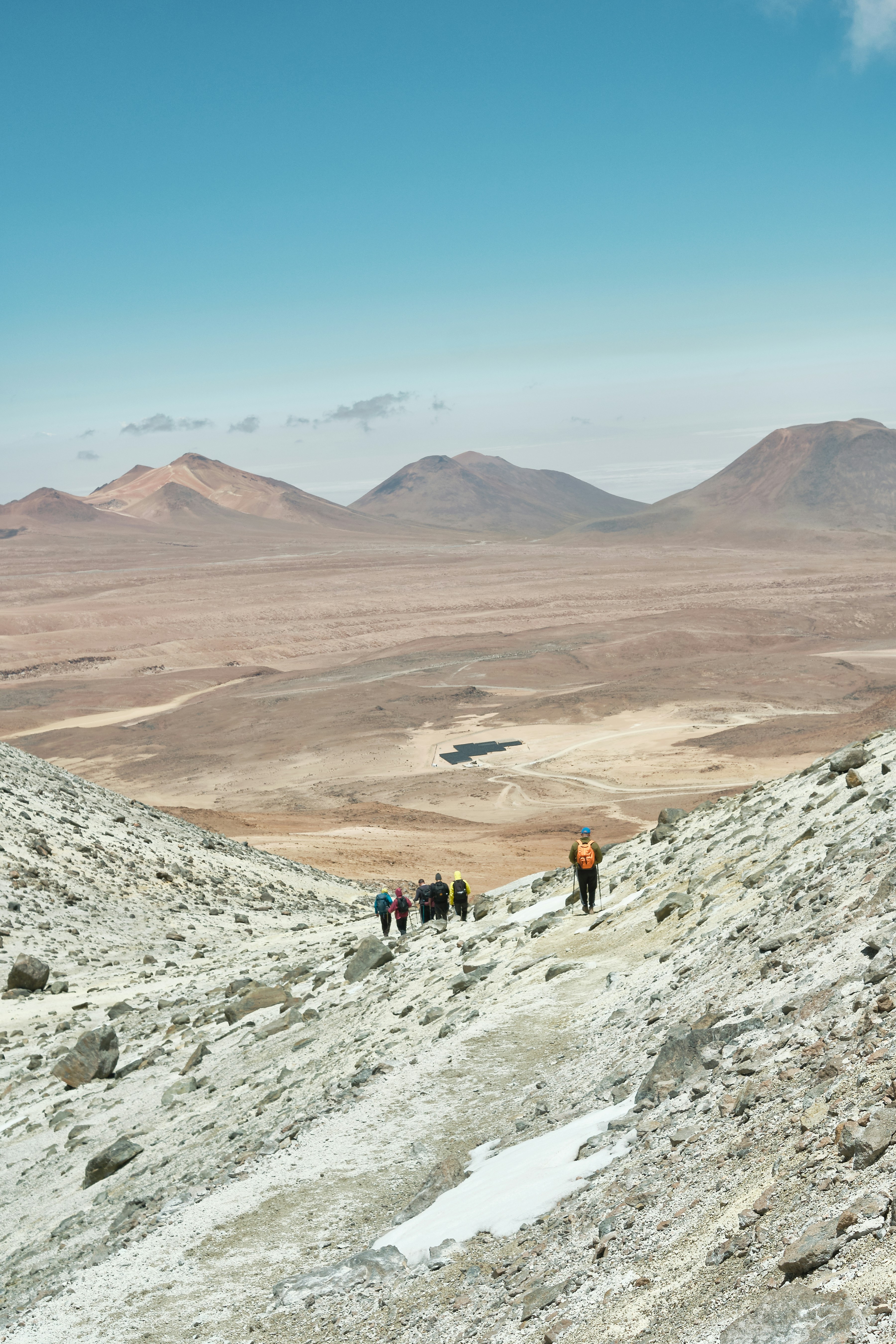Desert Ascent: Climbers Crossing the Sloped Expanse Beneath Distant Volcanoes