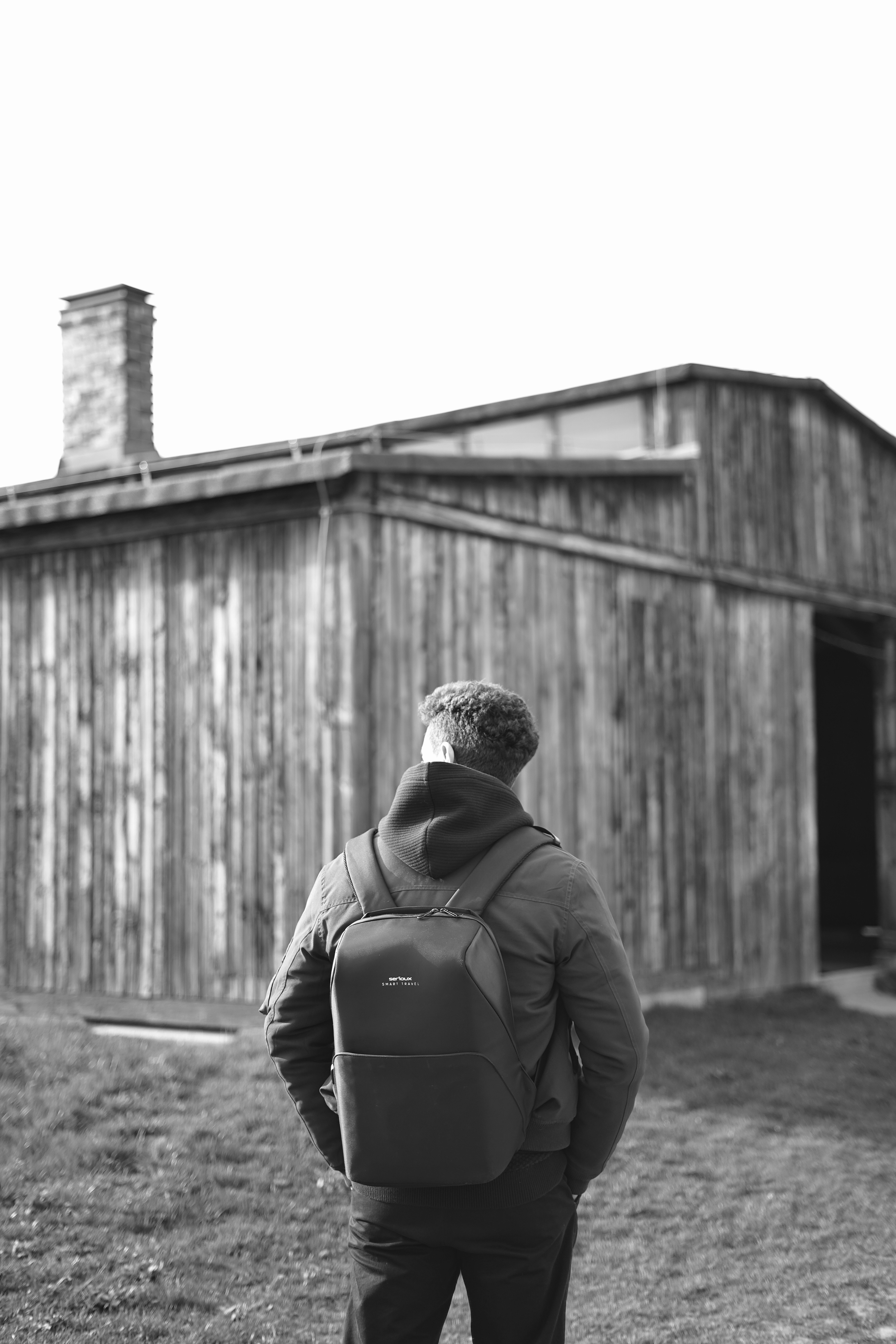 Backpack in Handcrafted Light: A Solitary Wanderer Before Weathered Barn