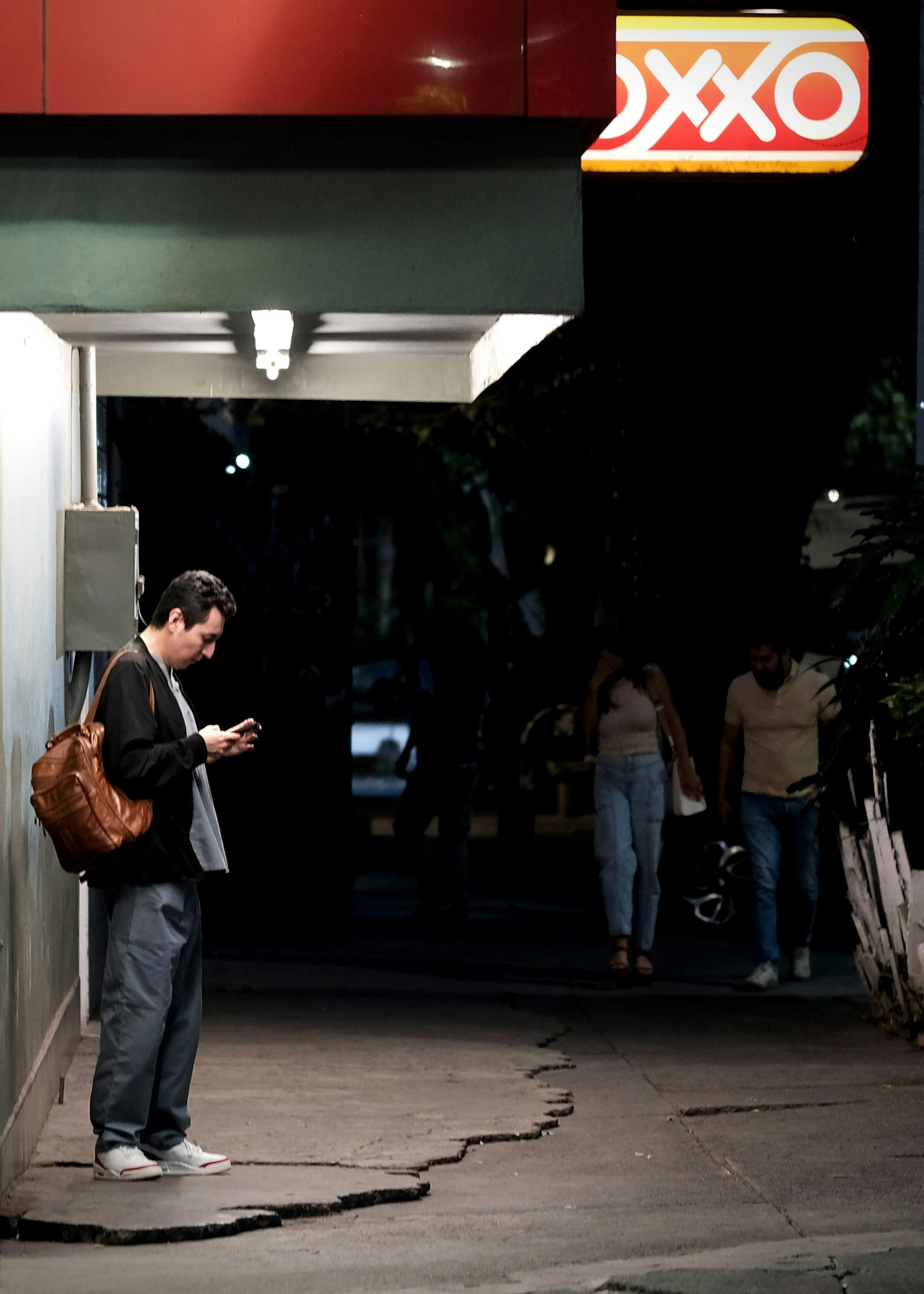 Midnight Stroll: A Man Glances at His Phone Outside a Brightly Lit Easthouse