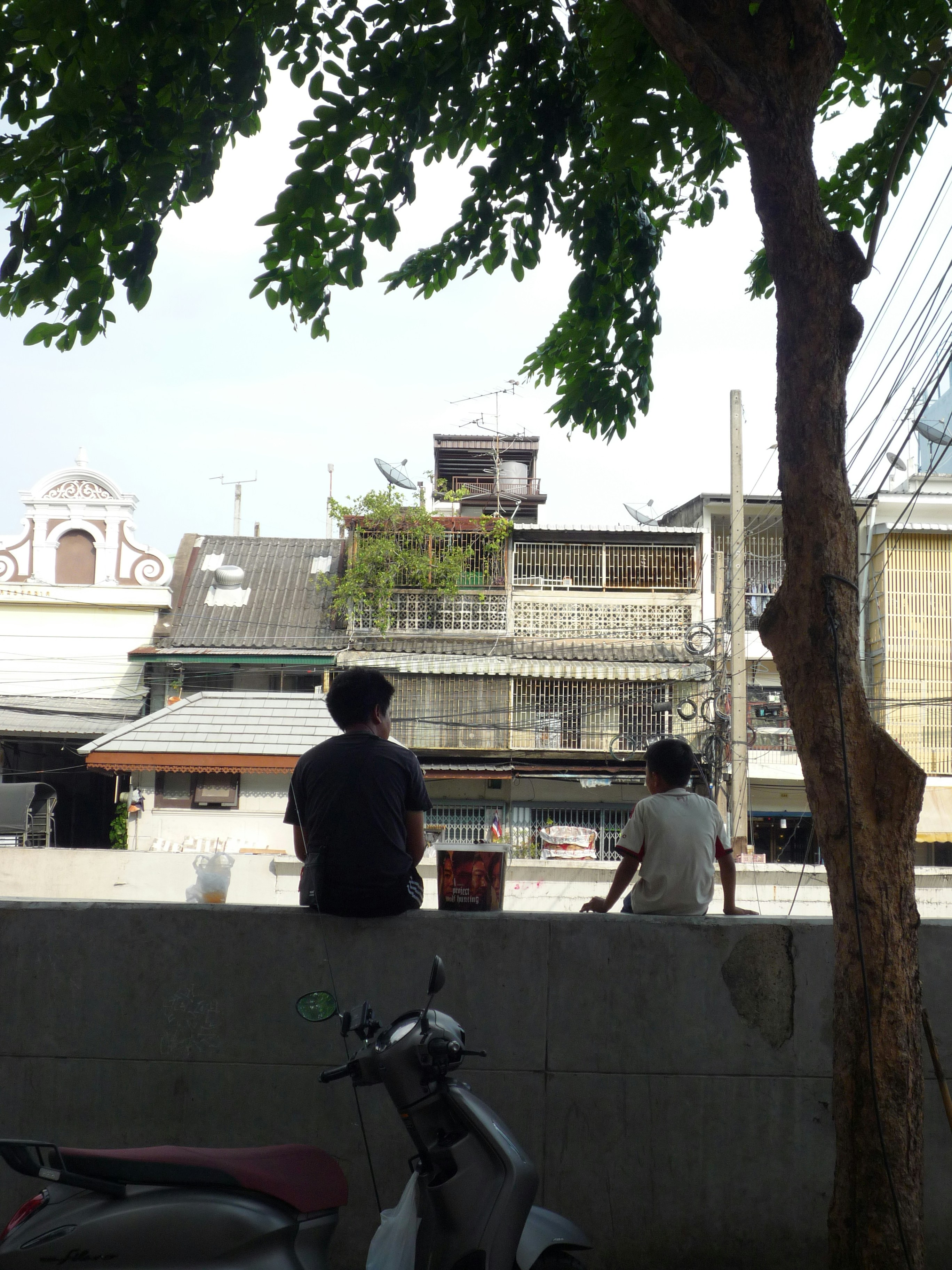 Two silhouetted observers on a concrete barrier overlook a busy street