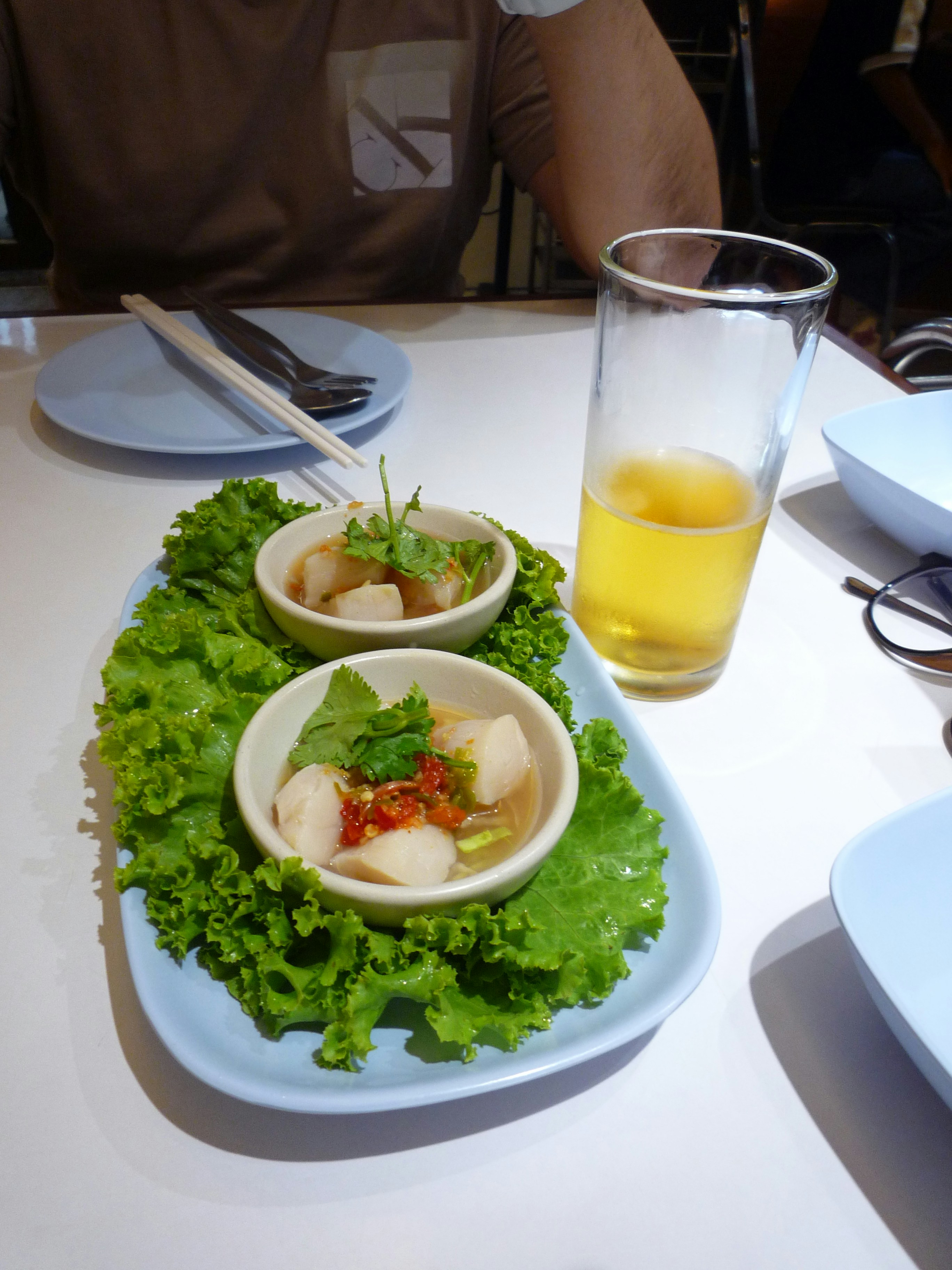 Two bowls of savory scallops on a bed of lettuce with a tall beer glass overhead